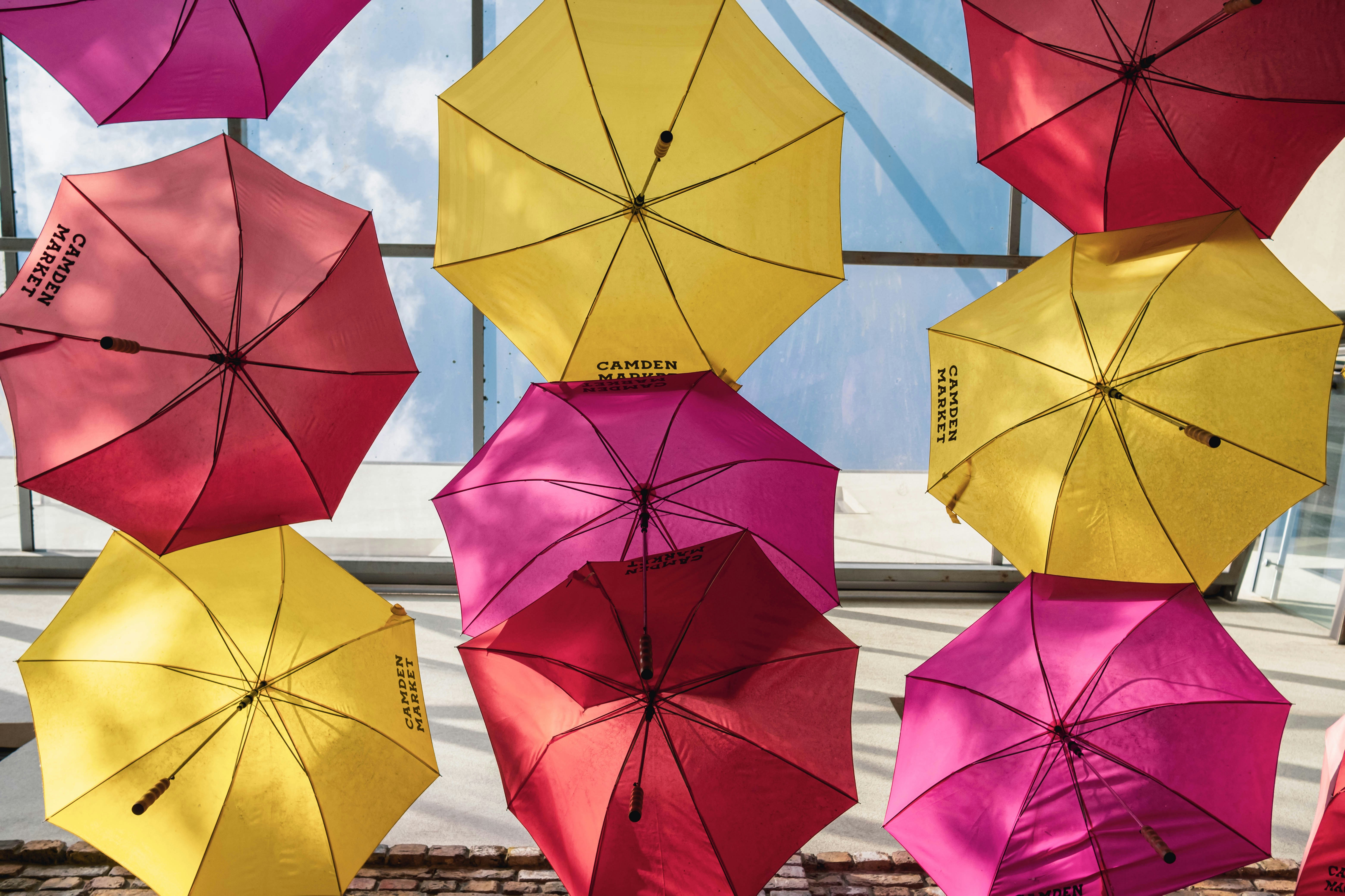 Colorful umbrellas in pink, yellow, and red suspended against a clear blue sky at Camden Market.