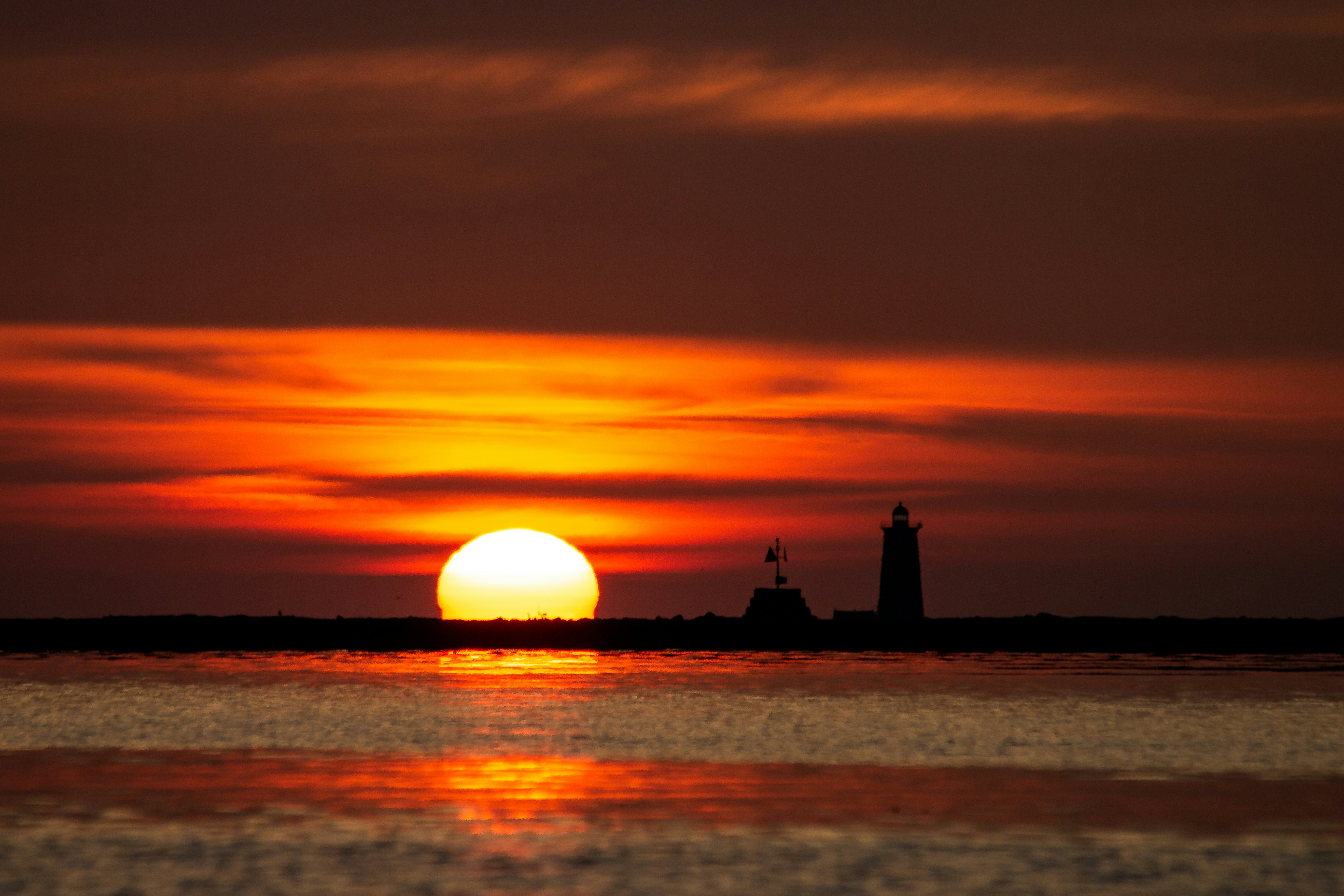 Silhouette of Whaleback Lighthouse against a vibrant sunrise on the ocean horizon.