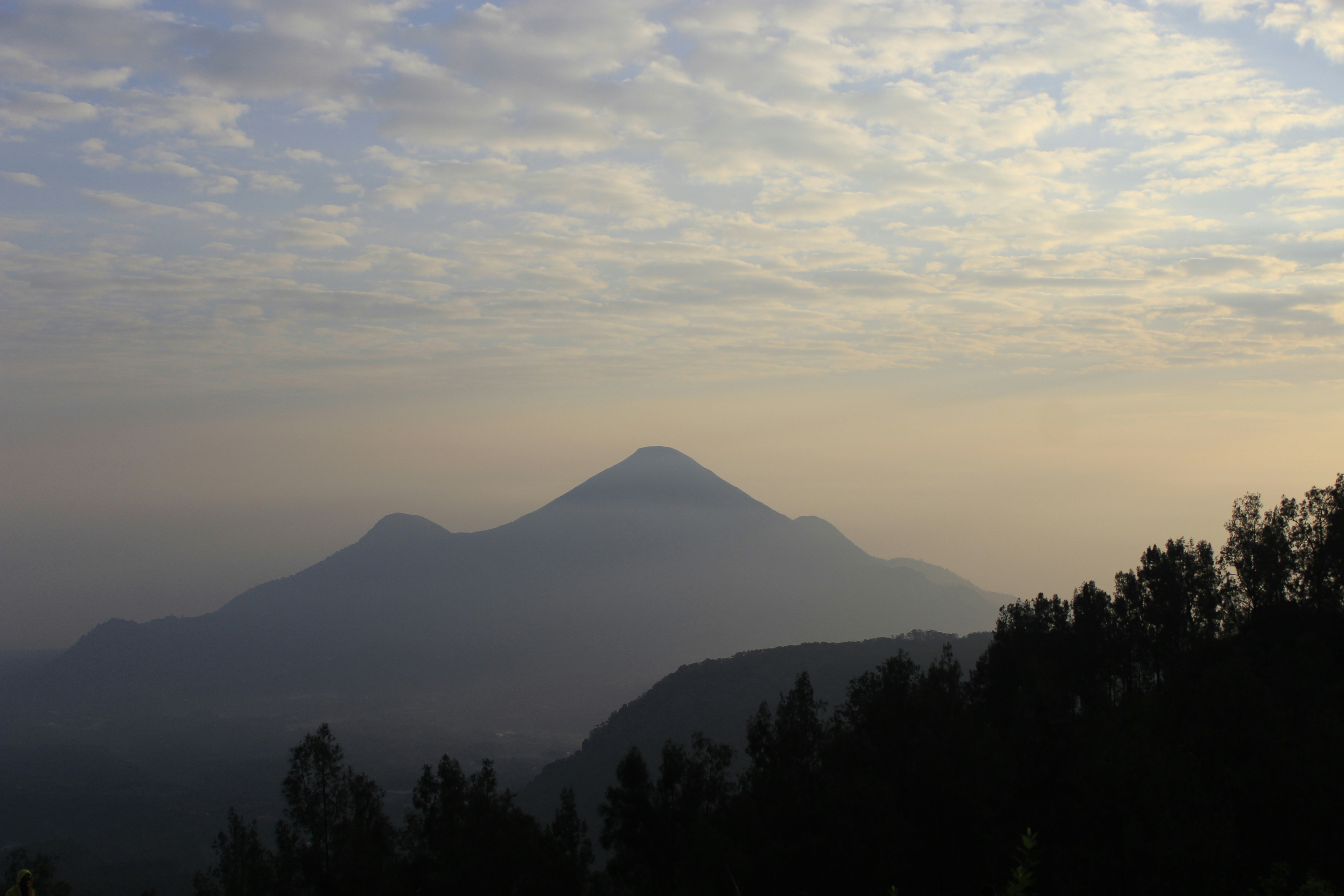 Hazy mountain silhouette against a softly lit morning sky with scattered clouds.