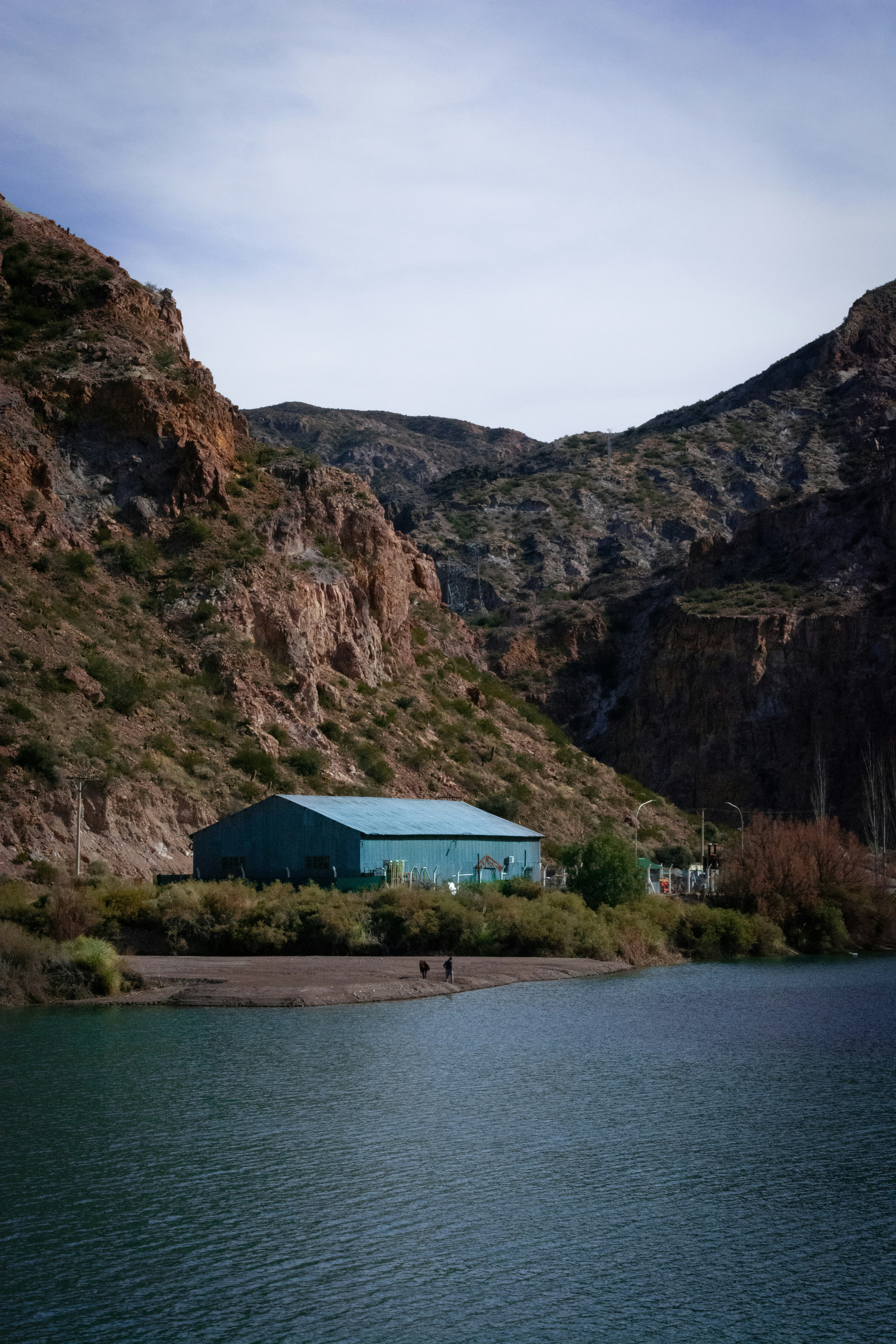 Blue-roofed warehouse by a tranquil reservoir tucked in a rocky gorge