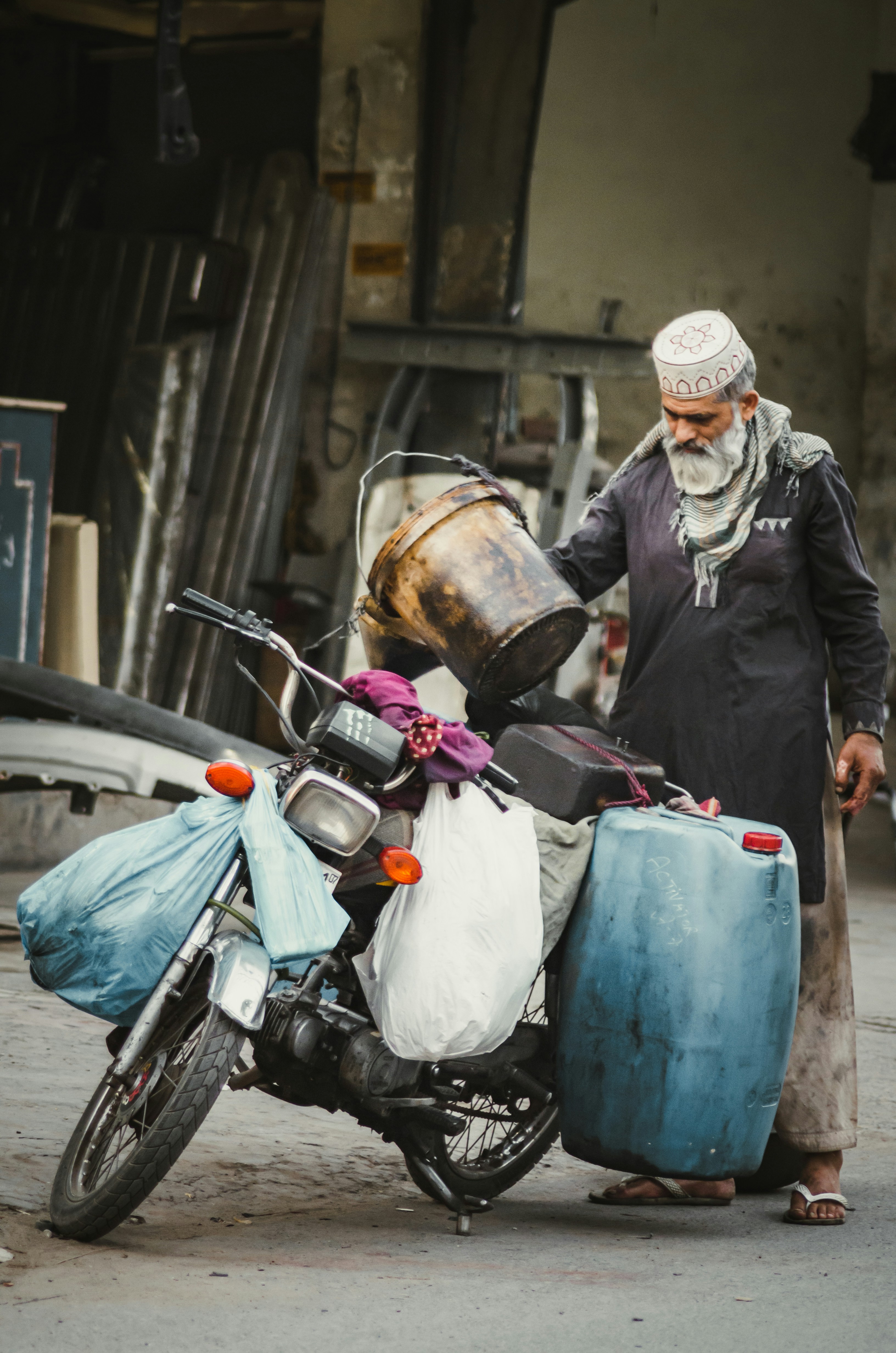 Cargo and Composure: A Bearded Traveler Tends a Heavily Laden Motorcycle in a Cluttered Yard
