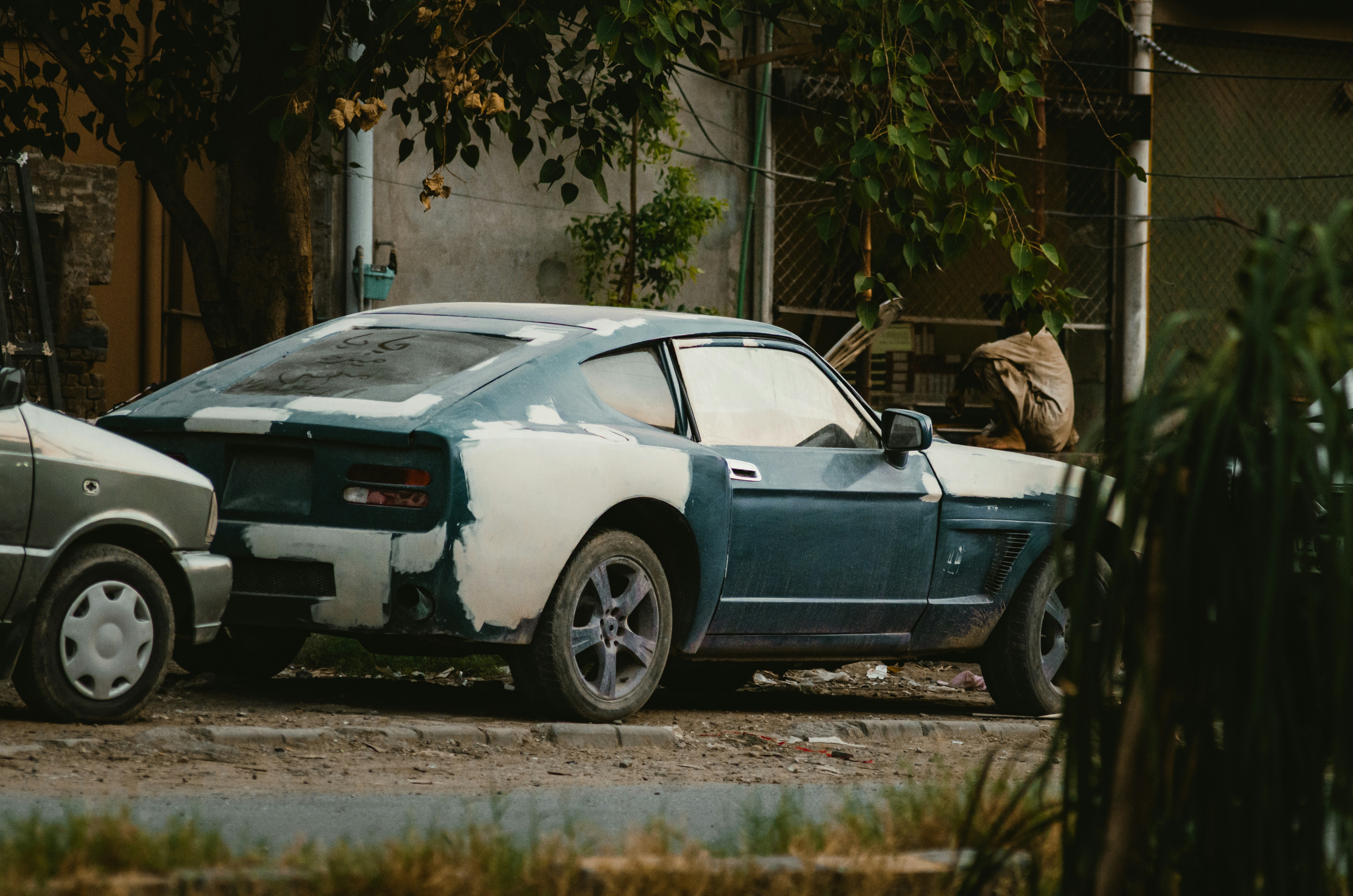 Vintage car undergoing restoration with mismatched panels parked on a street.