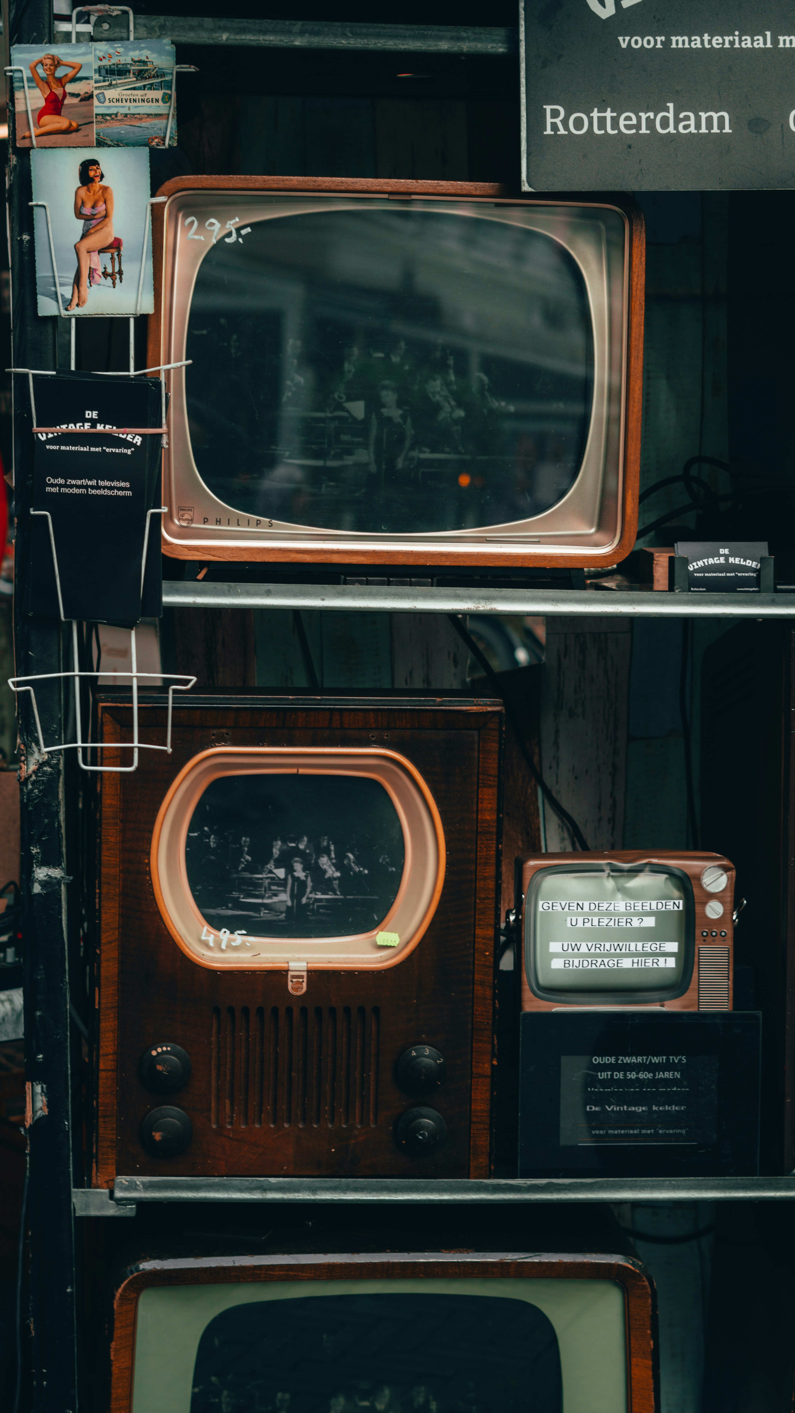 A collection of vintage televisions displayed on a market stall, showcasing the evolution of design and technology in broadcasting. The scene evokes a sense of nostalgia.