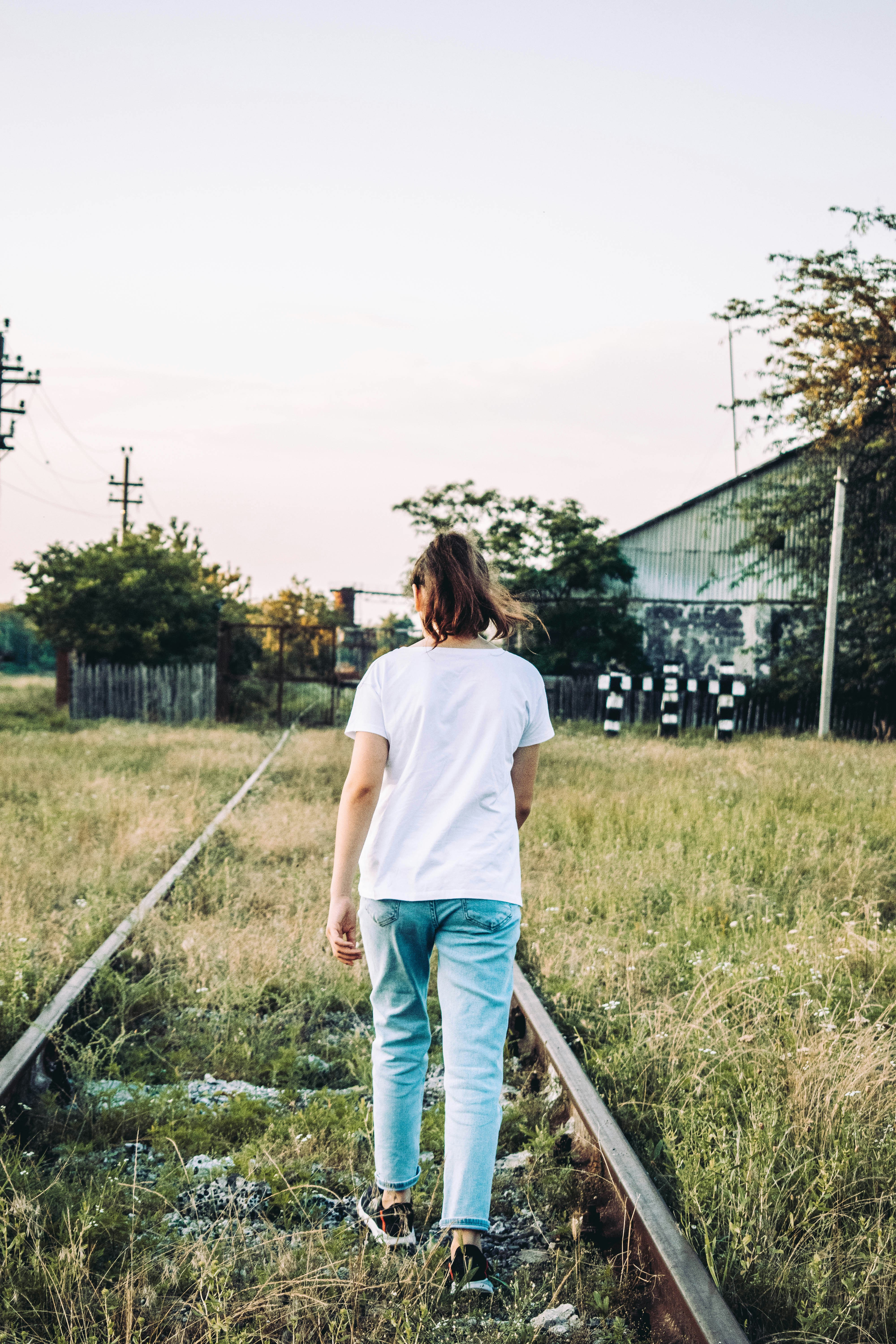 Woman in white t-shirt and blue denim jeans standing on train rail ...