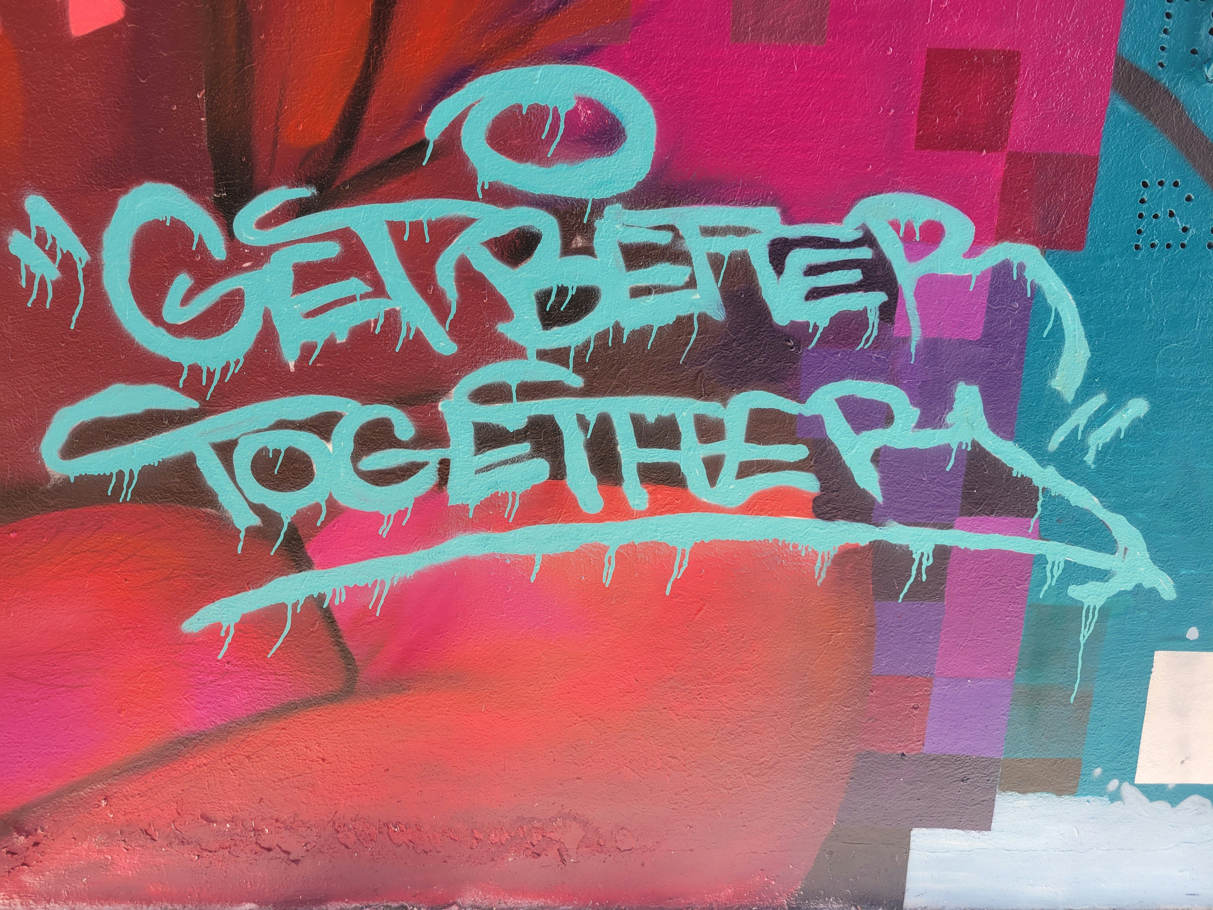Vibrant graffiti featuring the phrase 'Get Better Together,' emphasizing community and collaboration. The artwork showcases bold colors and fluid lettering.