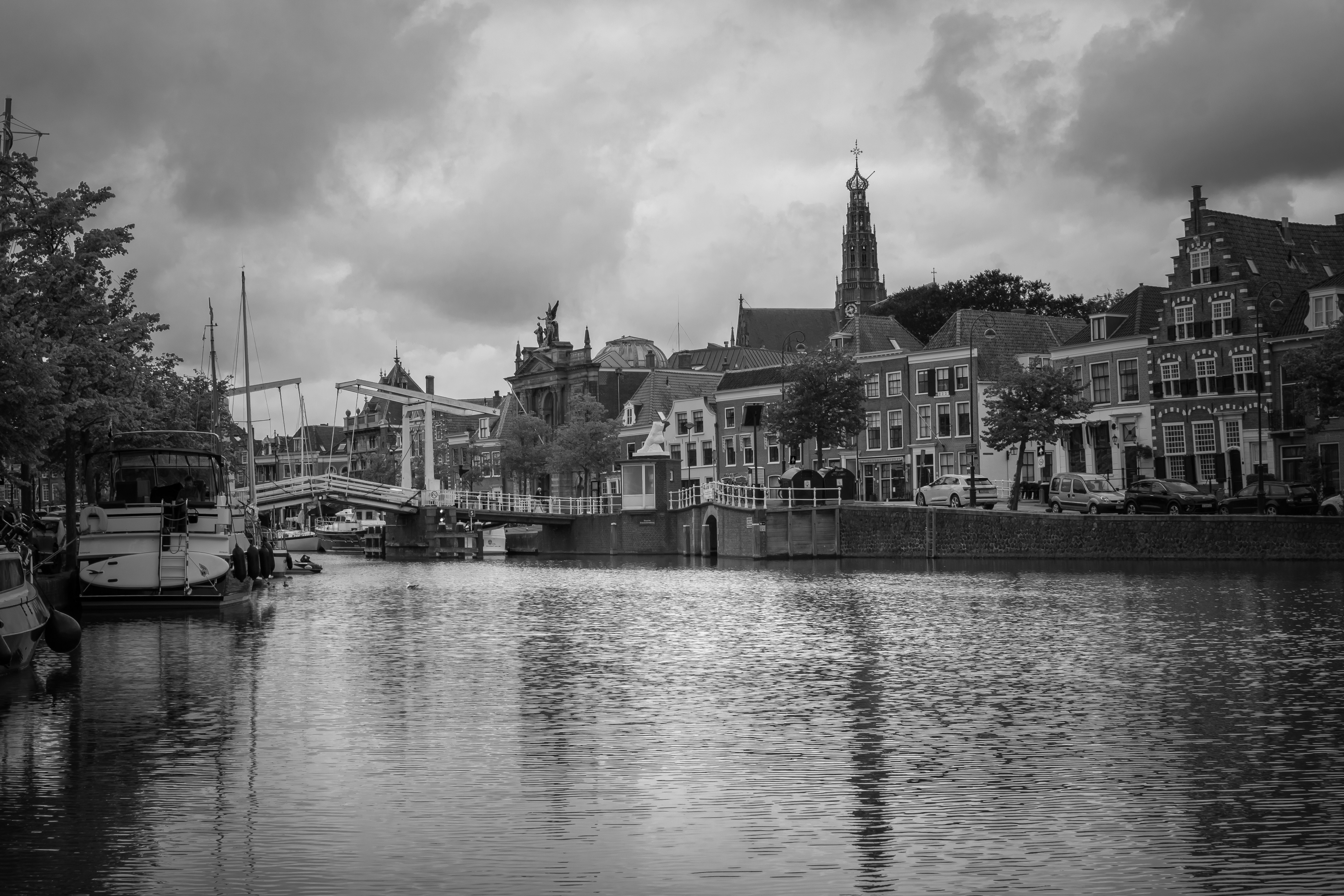 Grayscale view of a serene river flanked by historic buildings under a cloudy sky.
