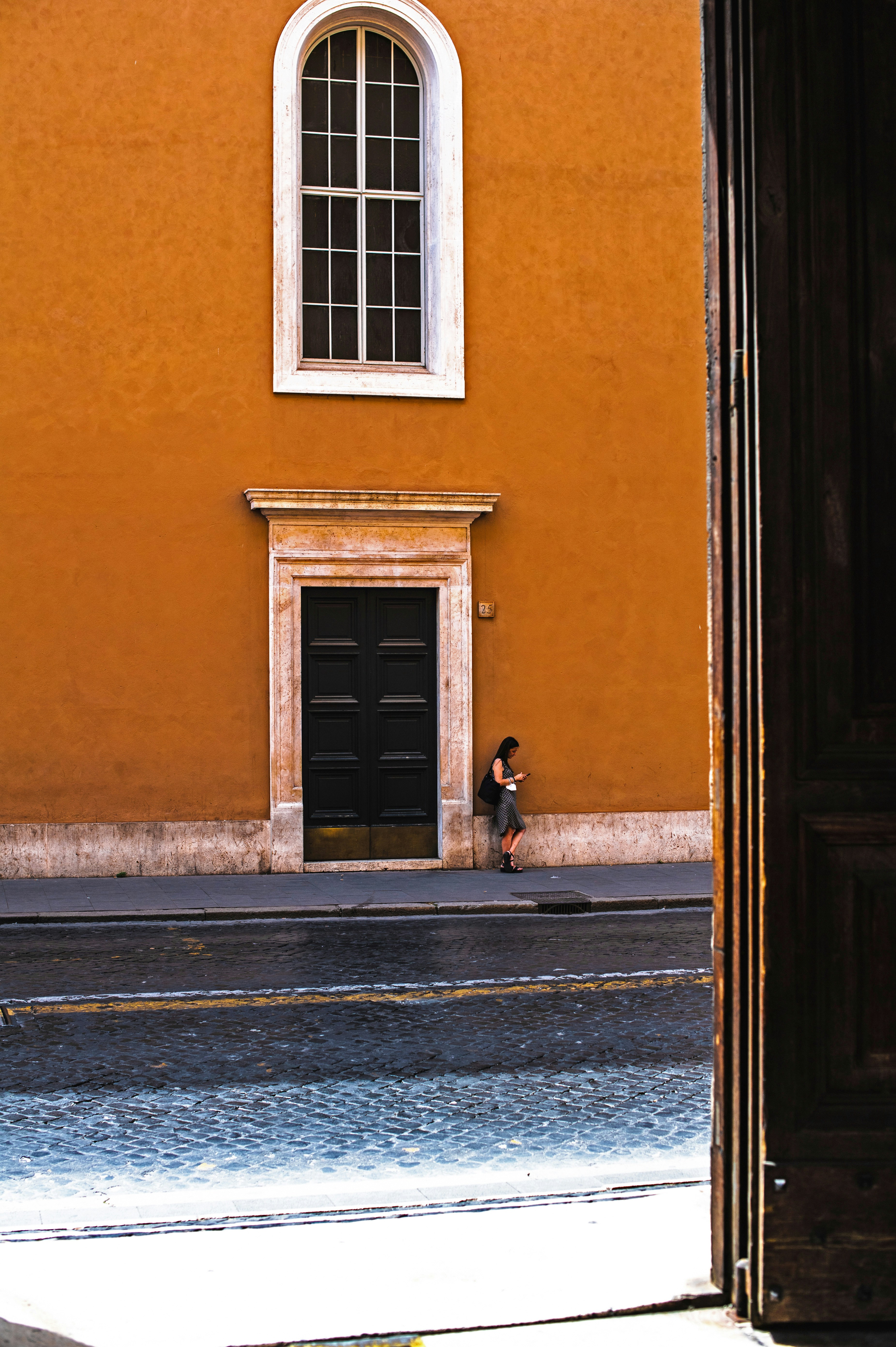 On the Verge of the Street: A Woman Pauses by an Orange Facade