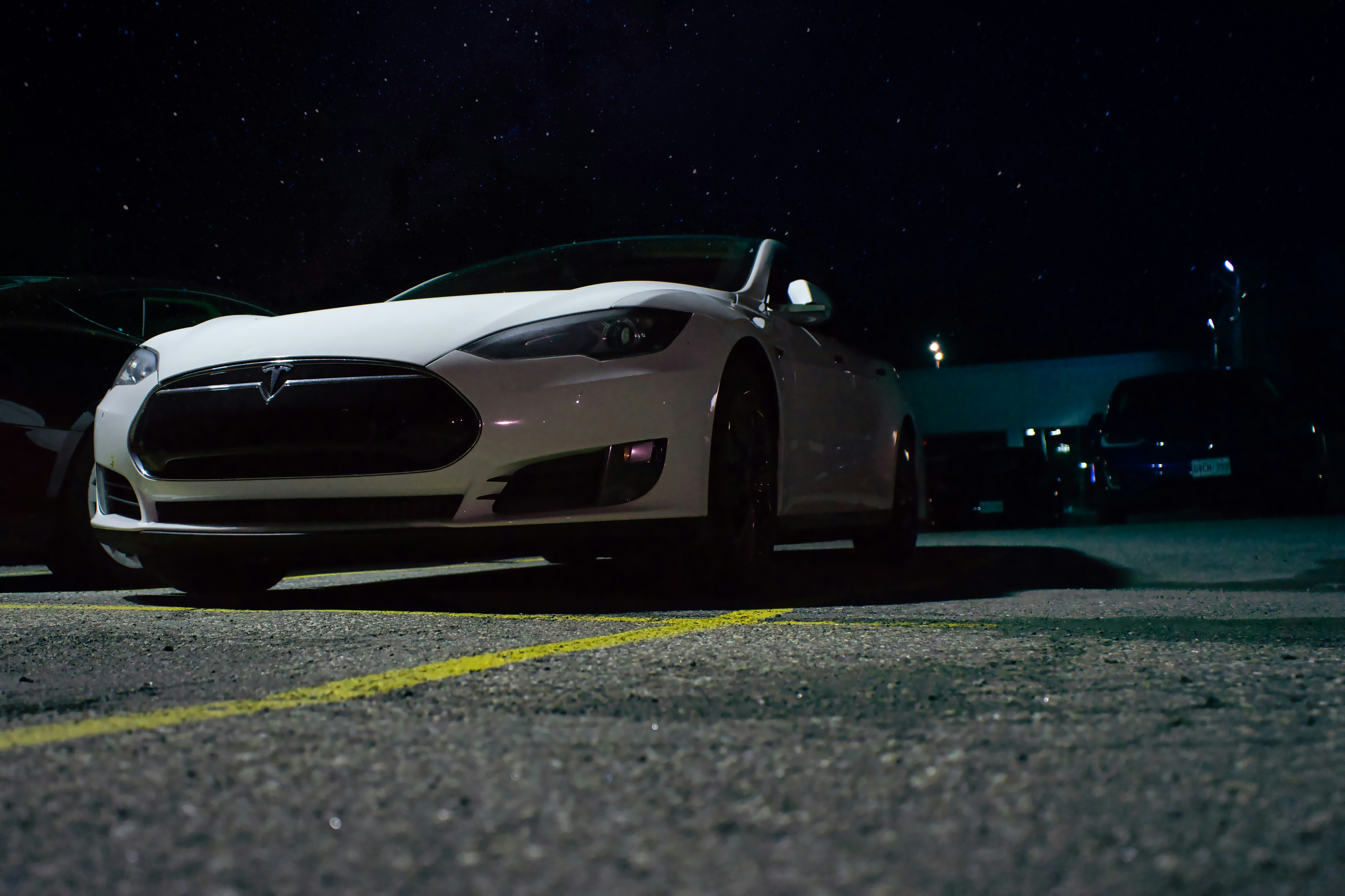 White Tesla Model S parked in a dimly lit lot, showcasing its sleek design against a starry backdrop.