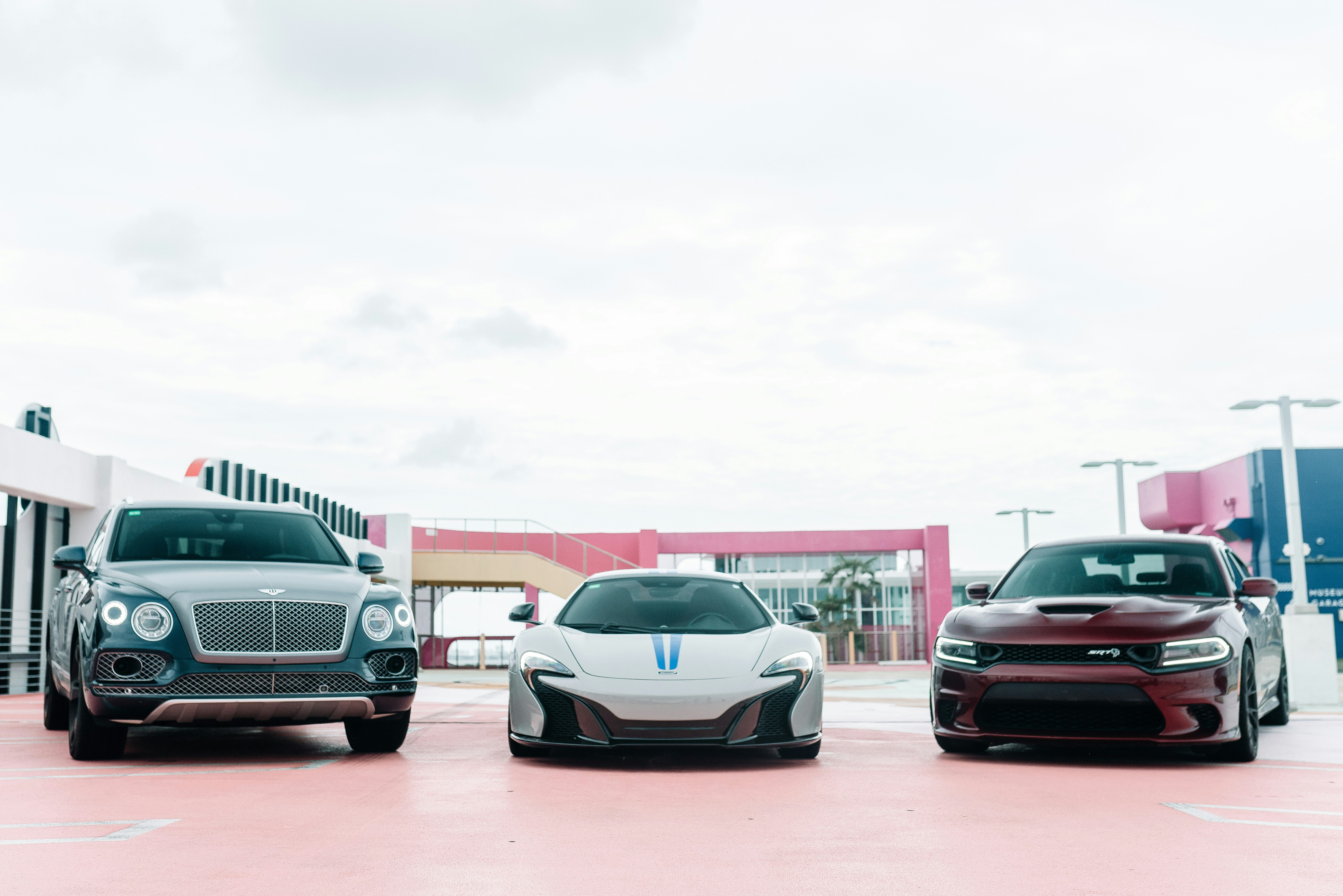 Three luxury cars parked in a modern outdoor setting under a cloudy sky.