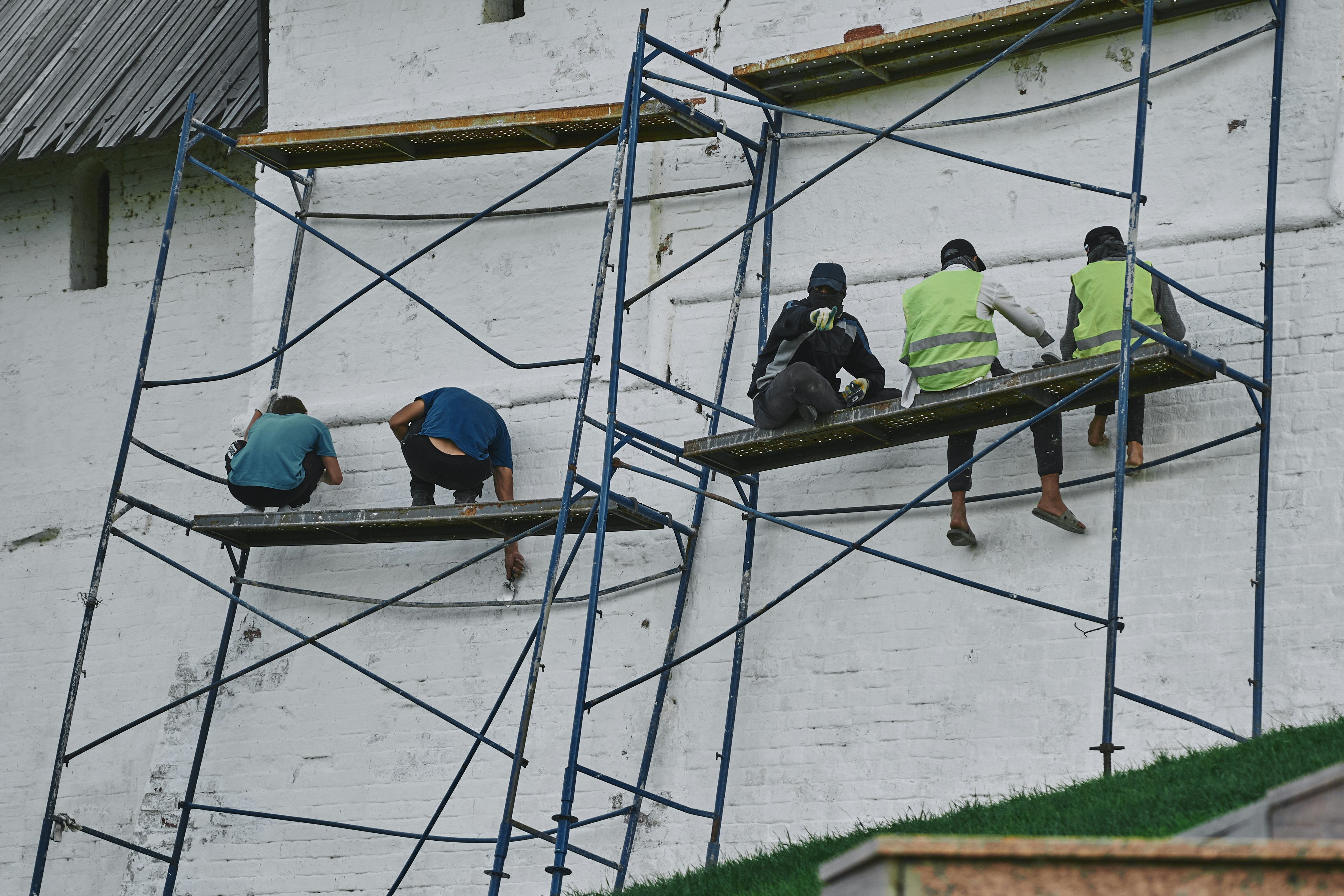 Workers on scaffolding meticulously restoring a historic wall, showcasing teamwork and dedication.