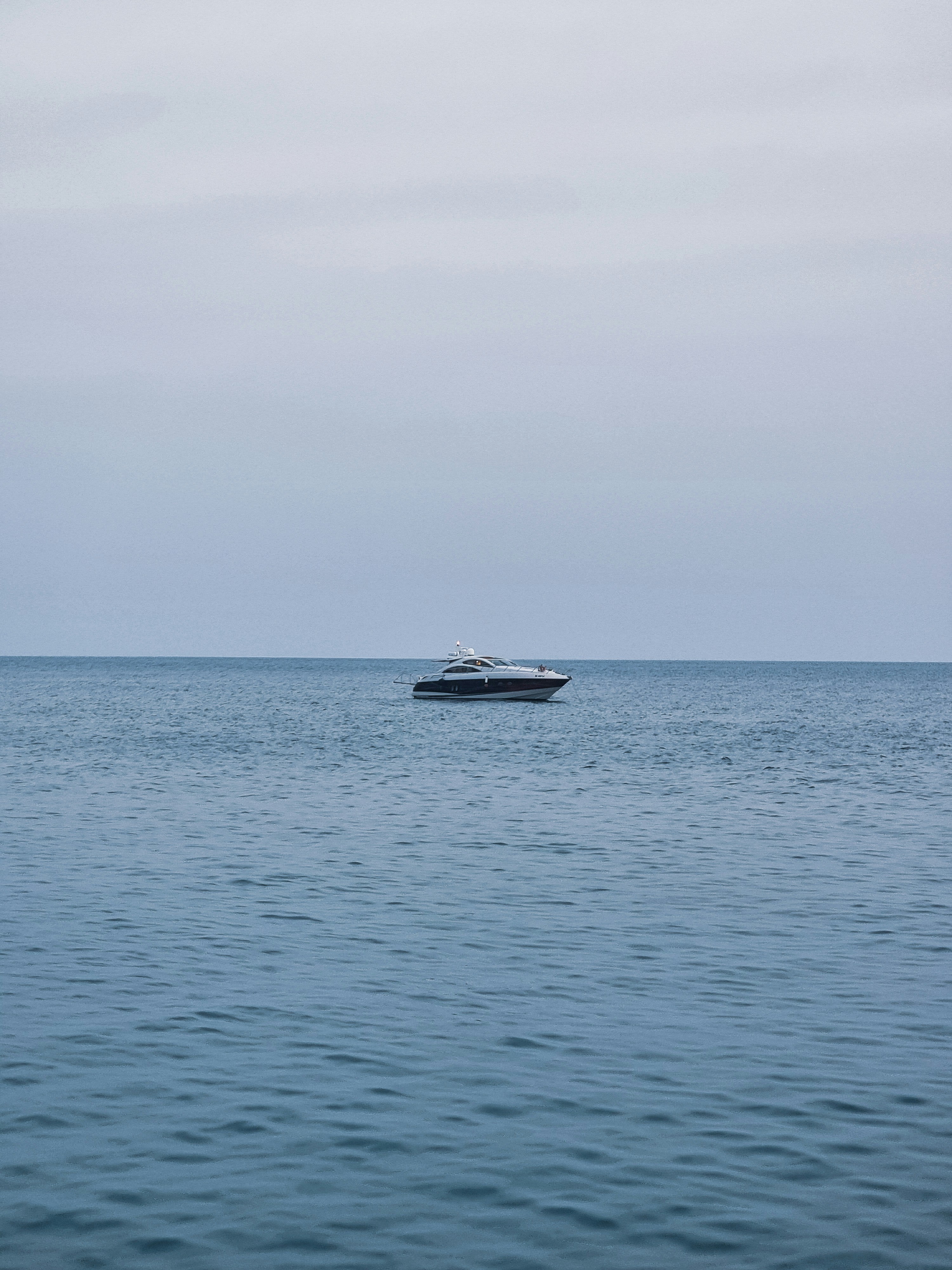 A sleek yacht floats peacefully on a calm sea under a soft, overcast sky.