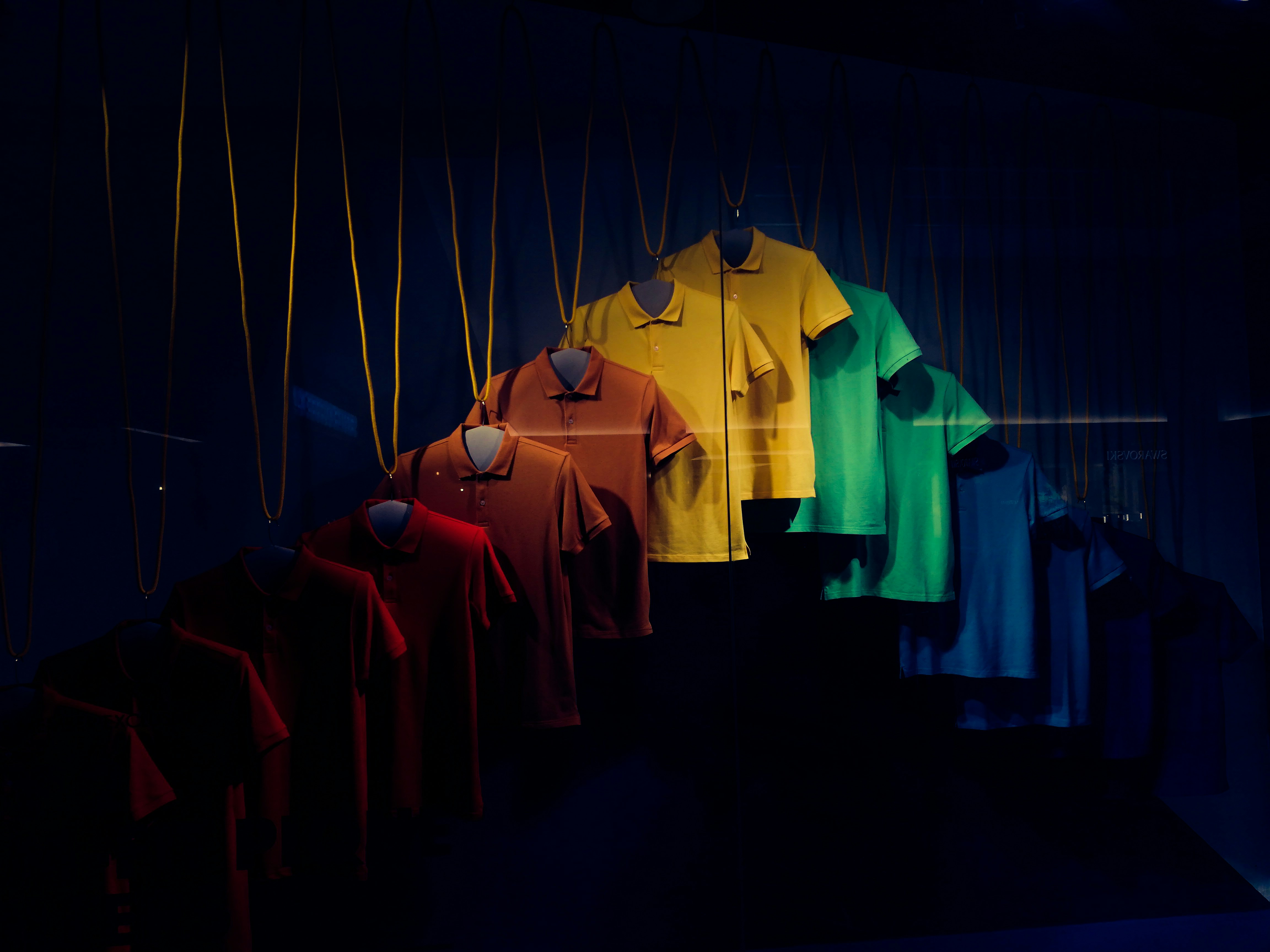 A vibrant arrangement of polo shirts in a gradient of colors, showcased against a dark backdrop, emphasizing the interplay of light and fabric textures.