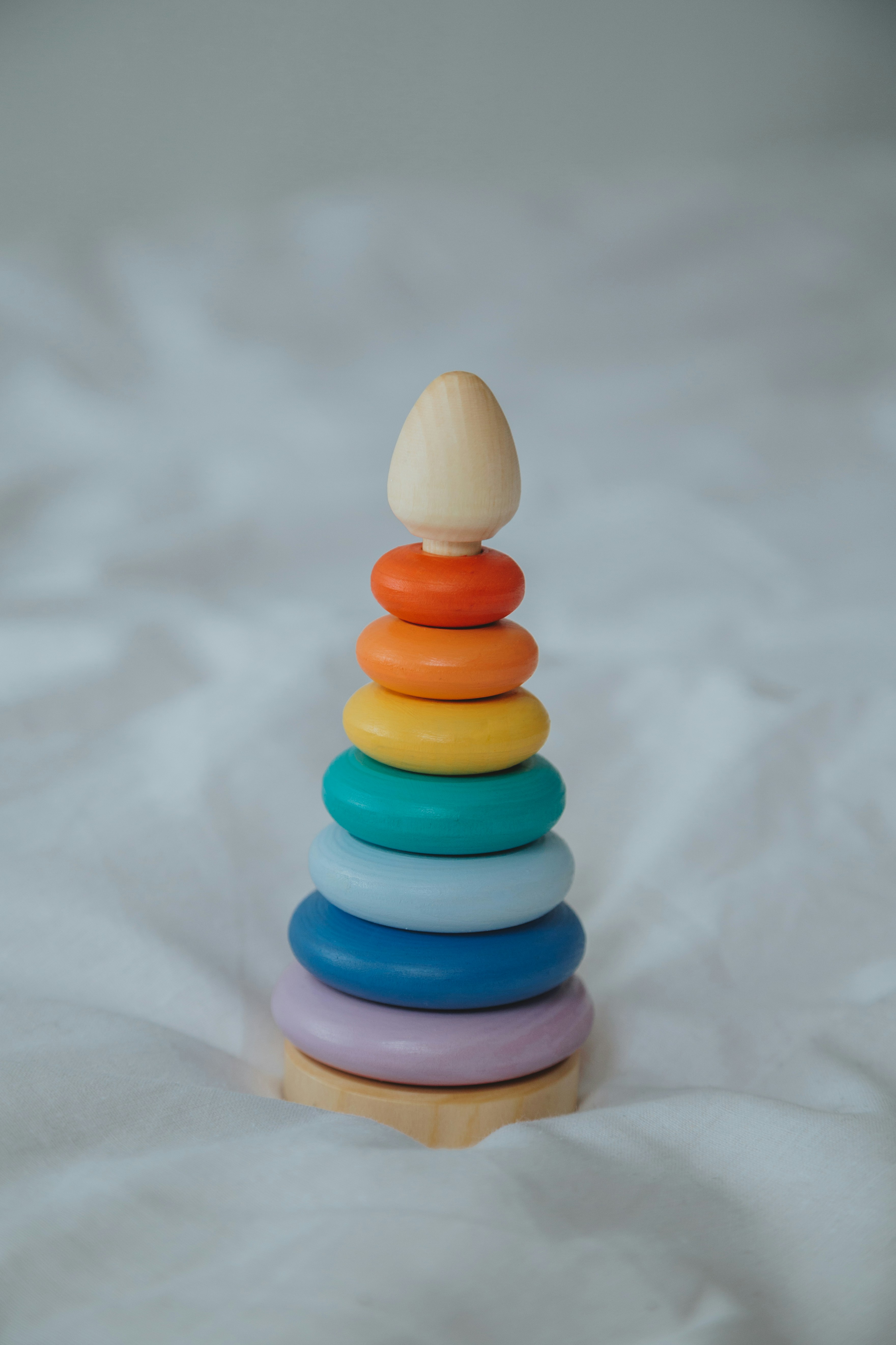 A vibrant wooden stacking toy featuring rings in various colors, arranged in a conical shape on a soft, white background.