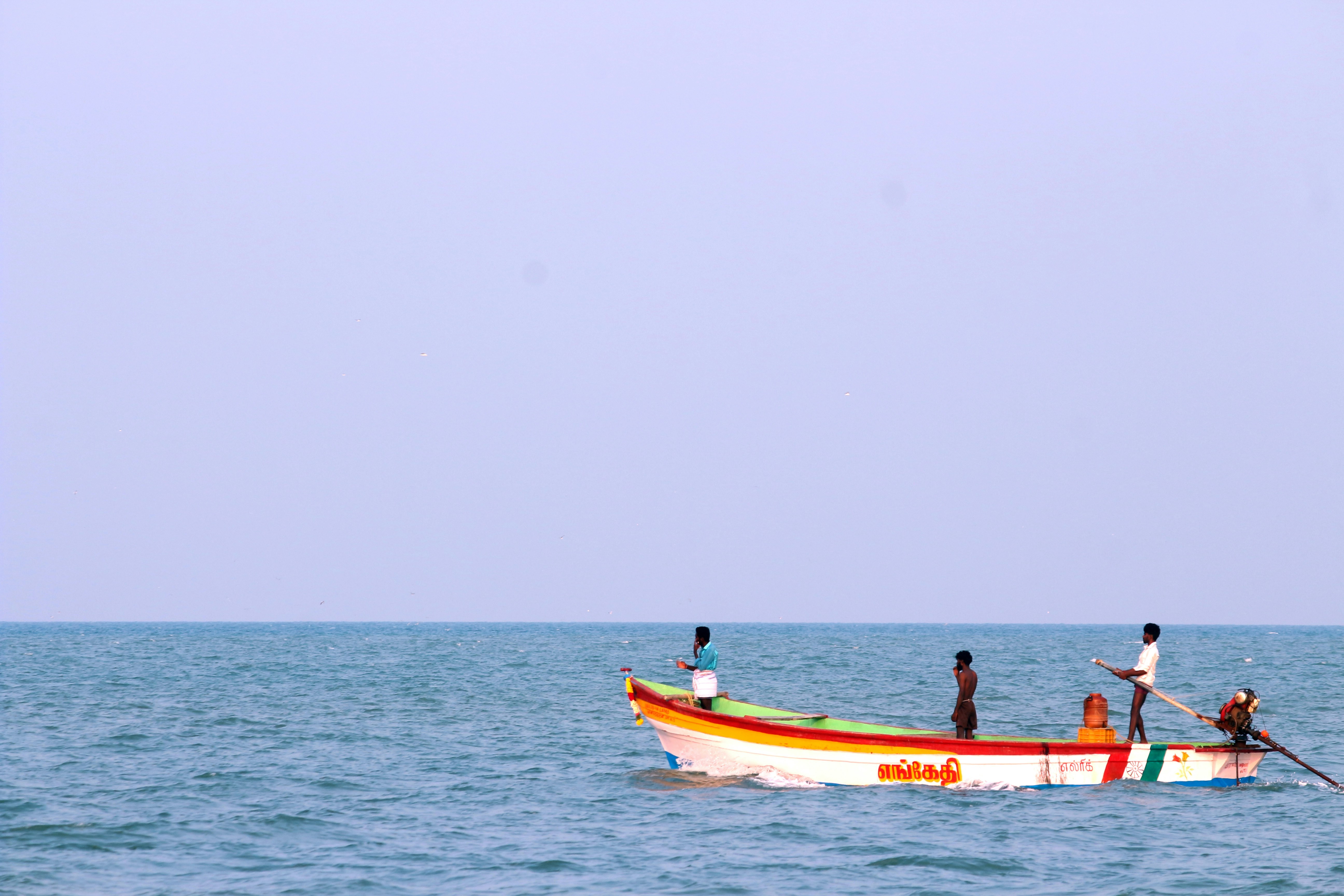 Fishermen navigating a colorful boat across a serene sea under a clear sky.