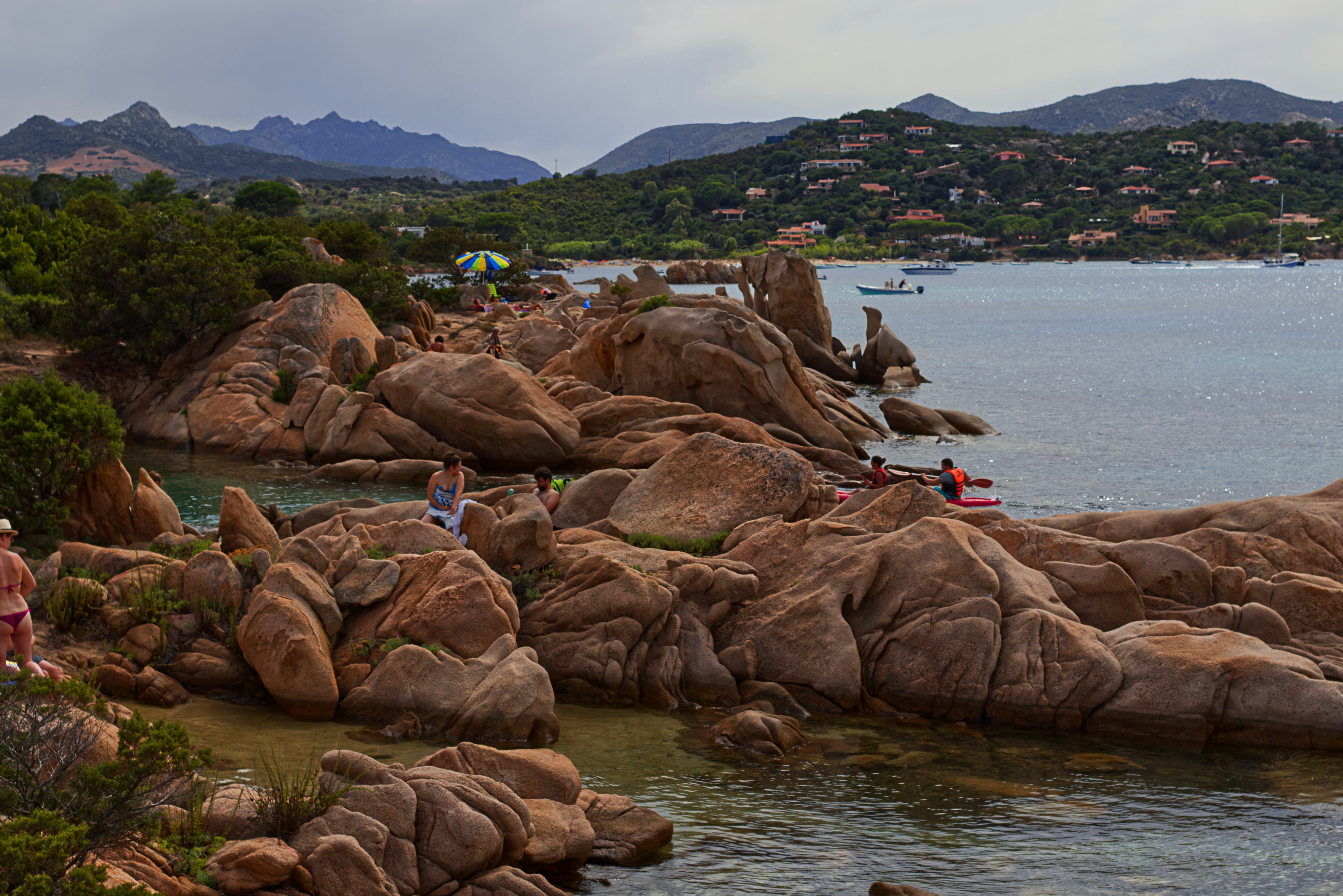 Kayakers navigate tranquil waters surrounded by rugged rocks and lush greenery, showcasing a peaceful coastal scene.