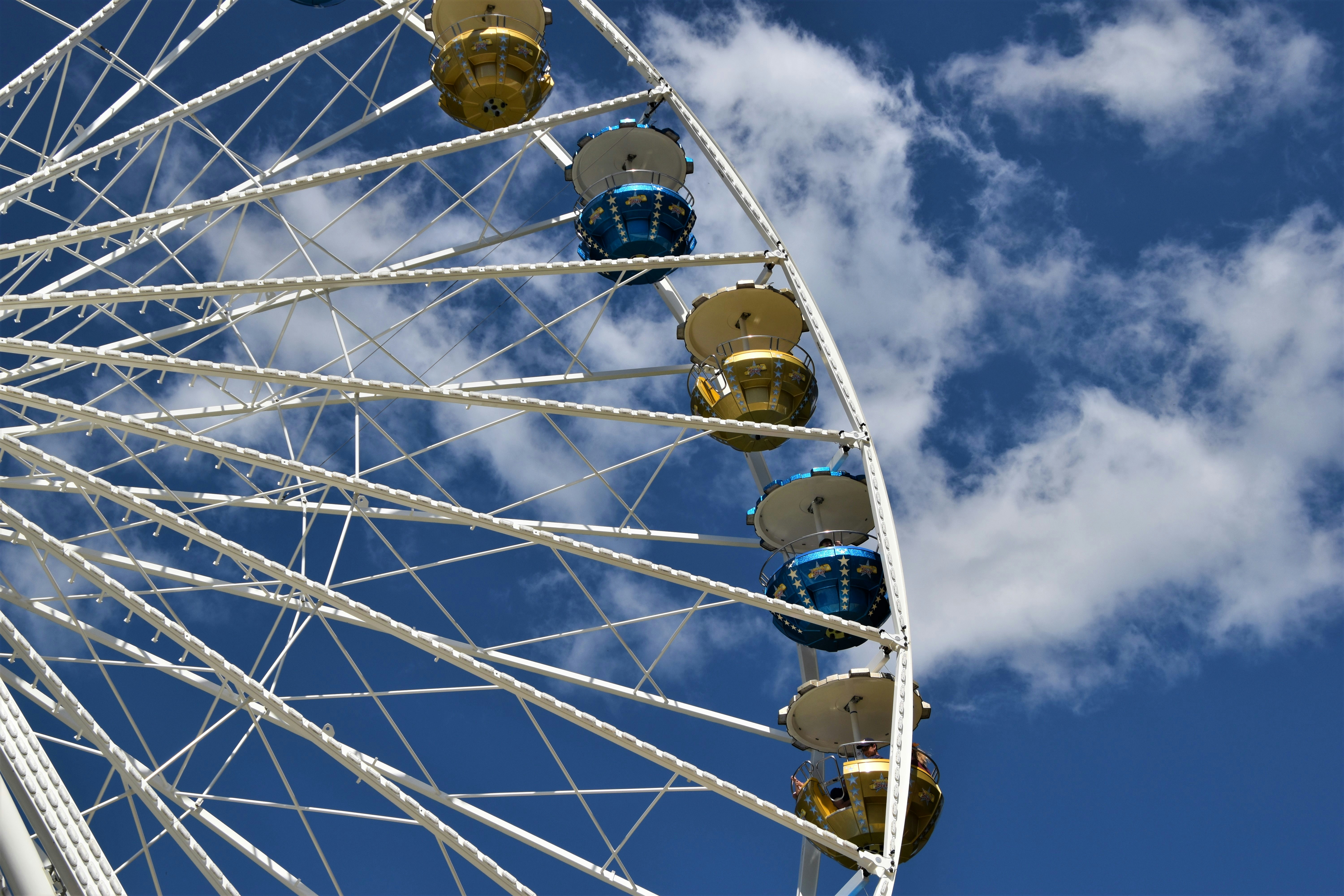 Vibrant ferris wheel cabins against a backdrop of blue sky and fluffy clouds.