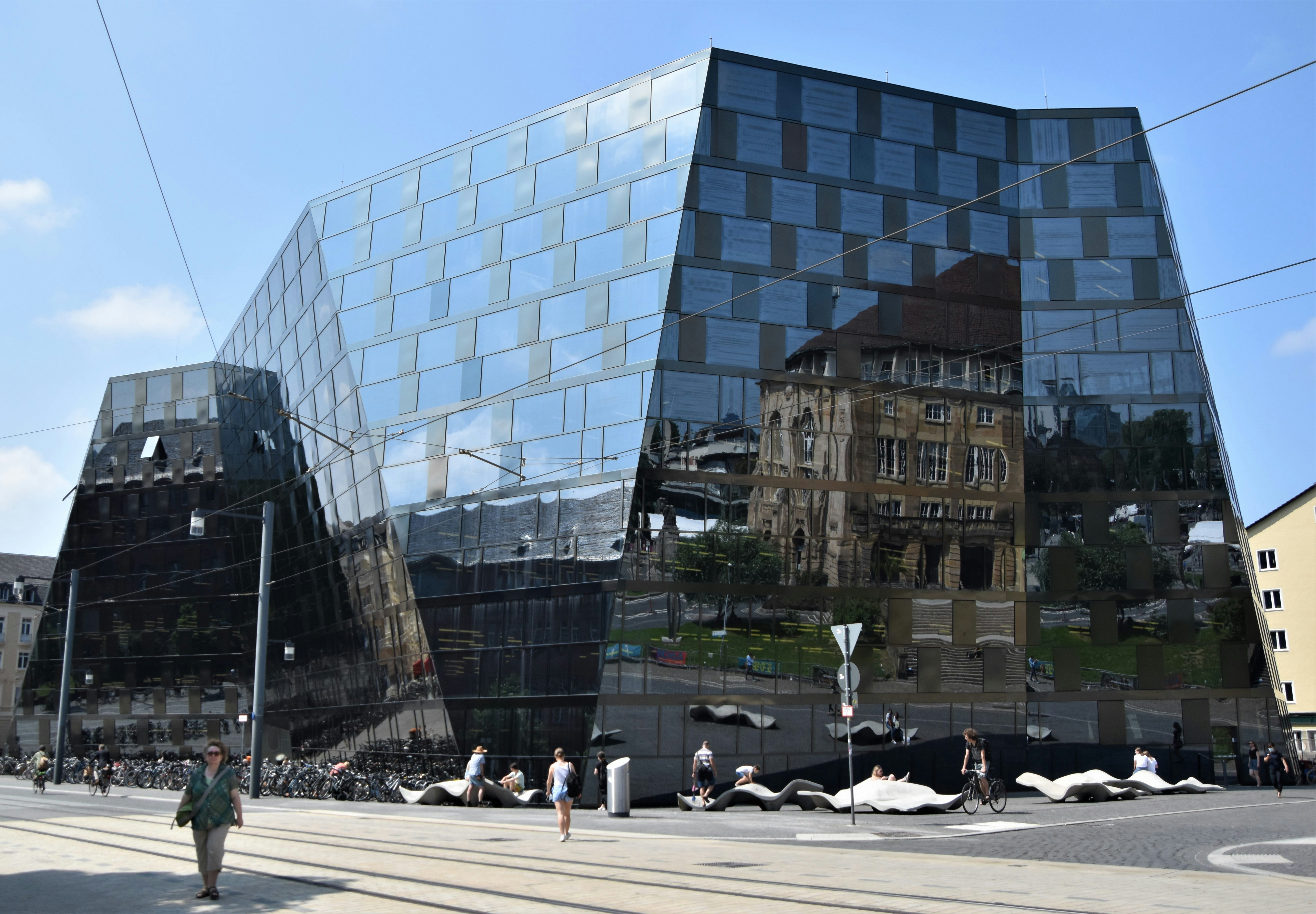 Modern glass building with reflective facade capturing surrounding structures under a clear blue sky.