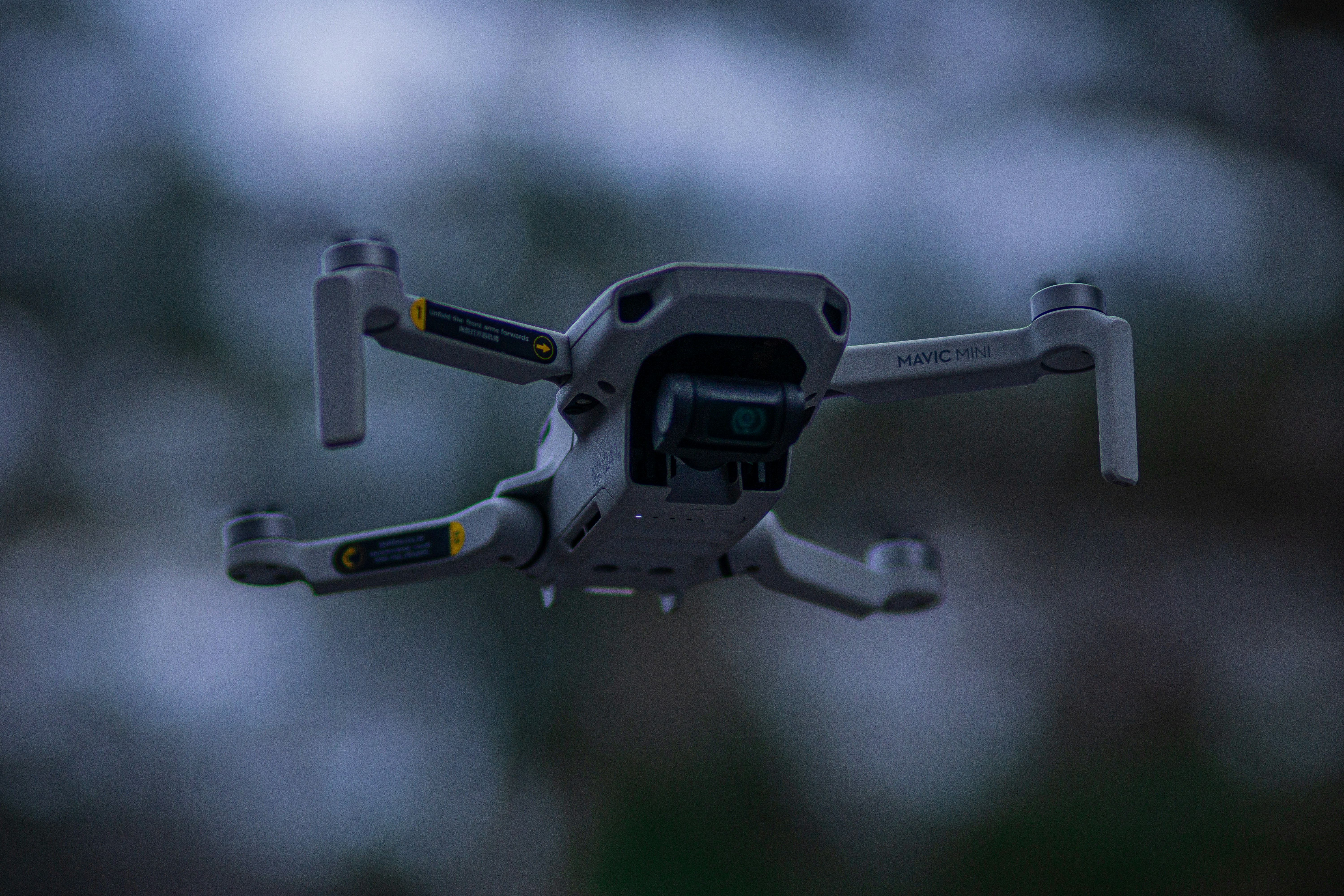 Gray and yellow quadcopter drone hovering with blurred natural background.