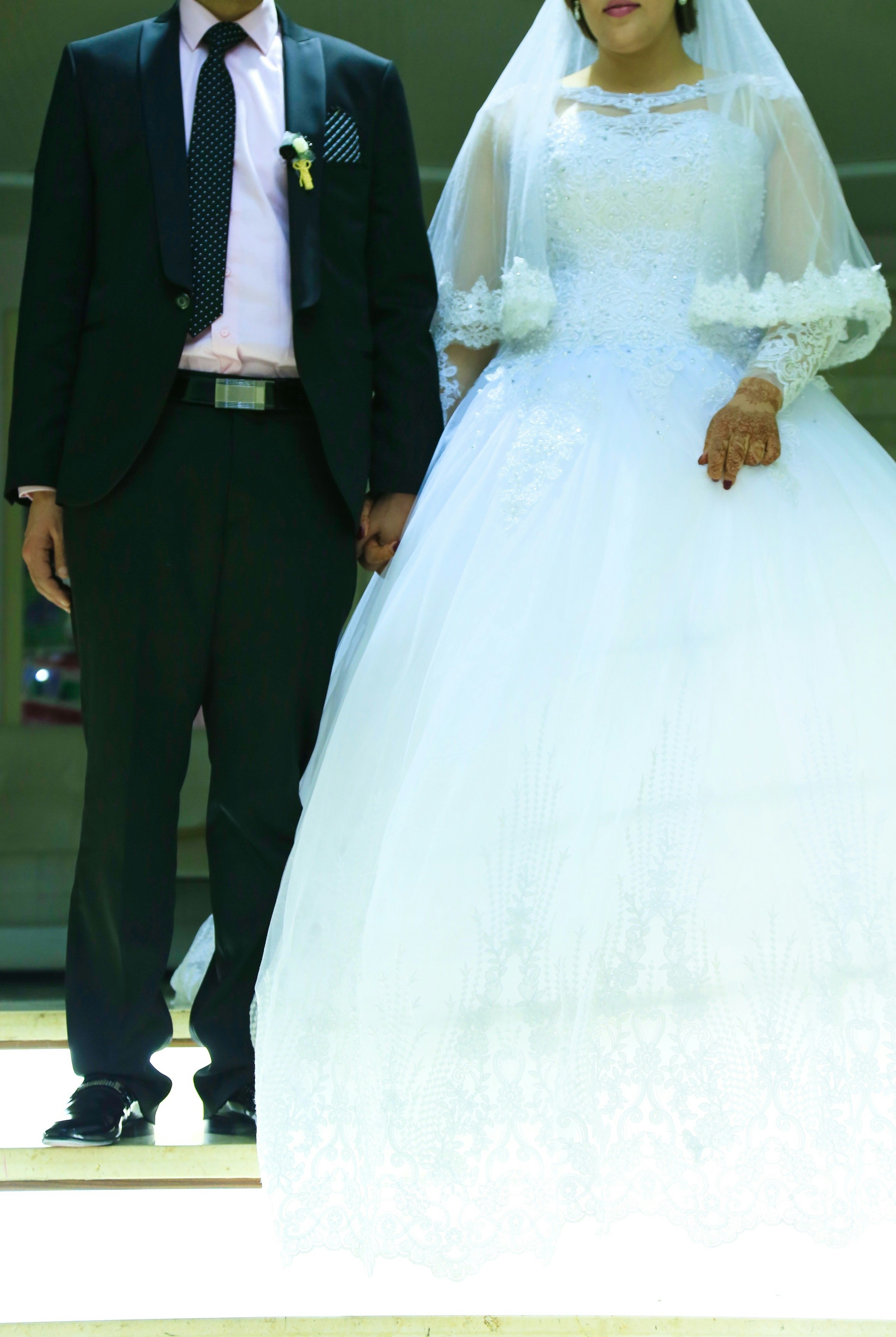 Couple holding hands in formal attire, showcasing a beautiful wedding dress and suit. The scene captures the essence of love and commitment.