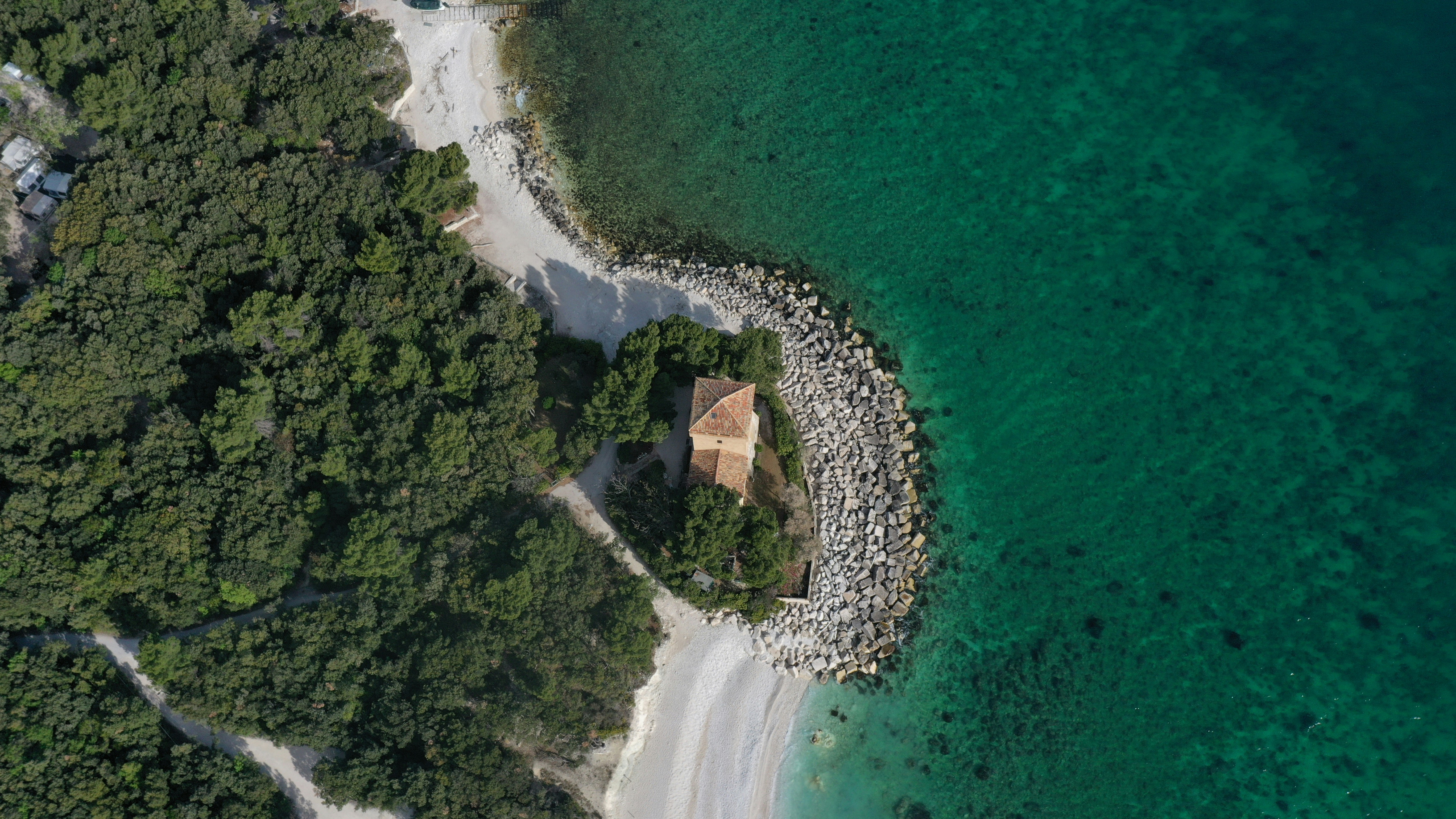 Aerial view of a rocky peninsula with dense green trees surrounded by clear turquoise water.
