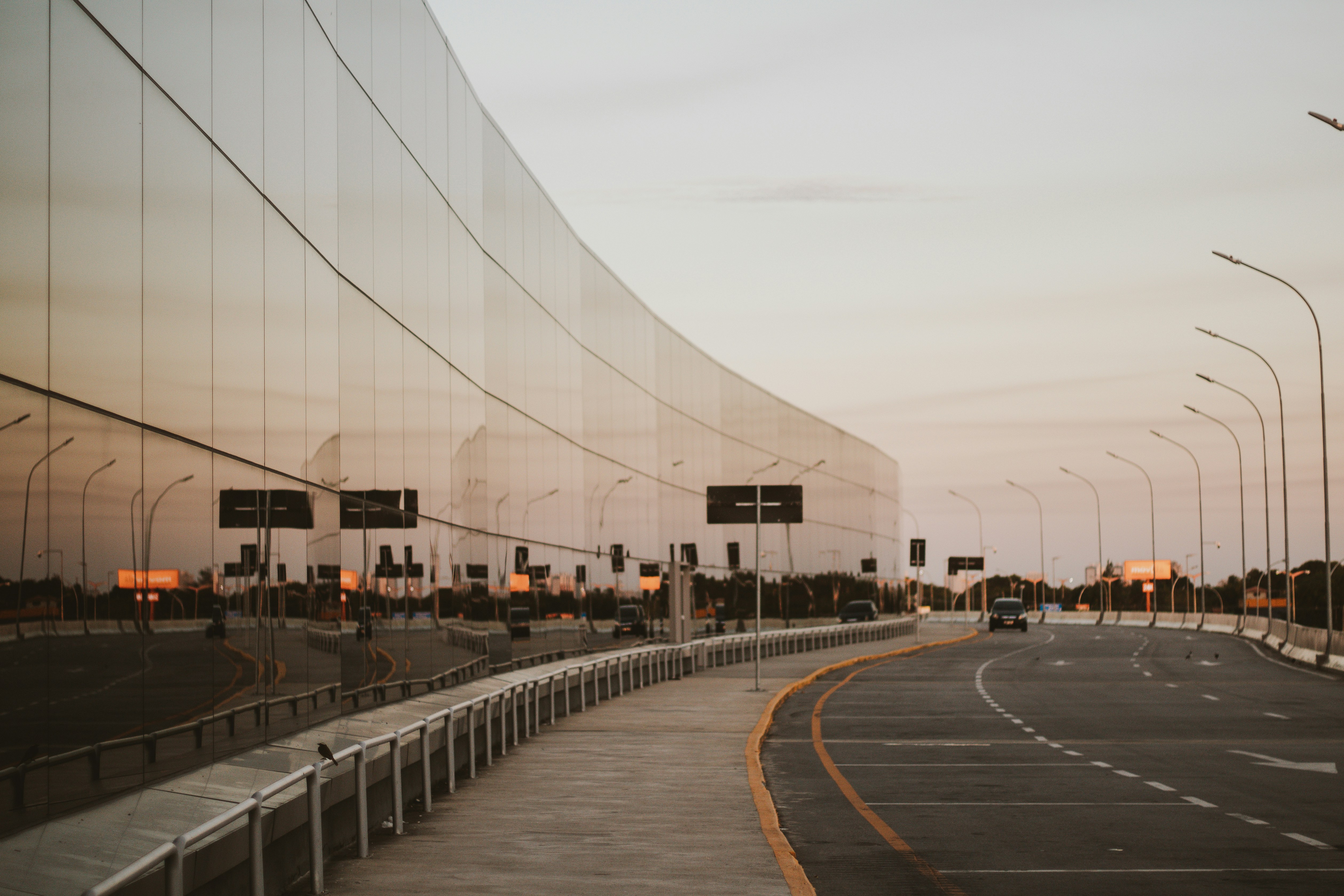 Curved highway with reflective glass barrier under soft evening light.