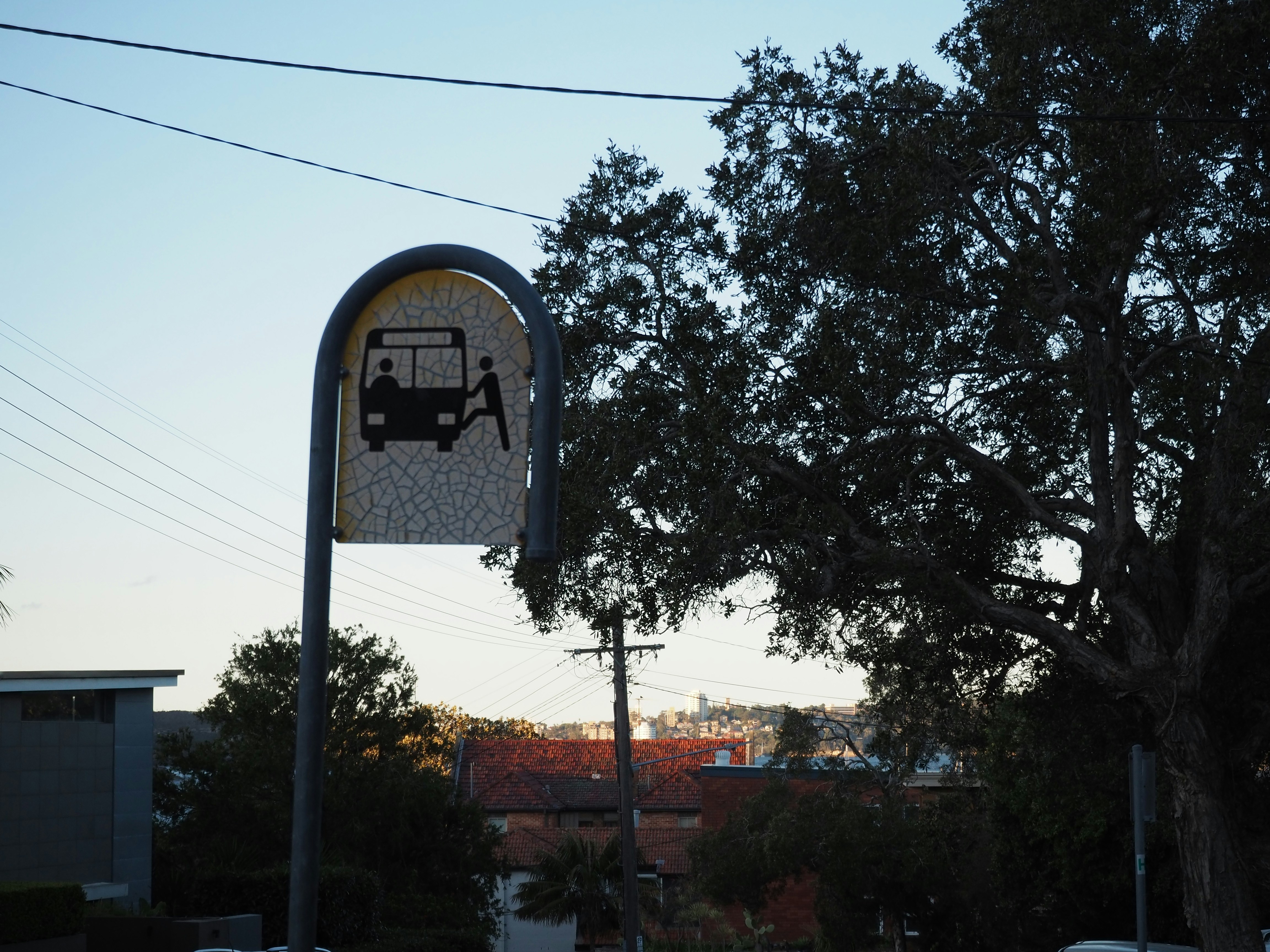 Stylized bus stop sign featuring a silhouette of a bus and a passenger, set against a backdrop of trees and urban architecture.