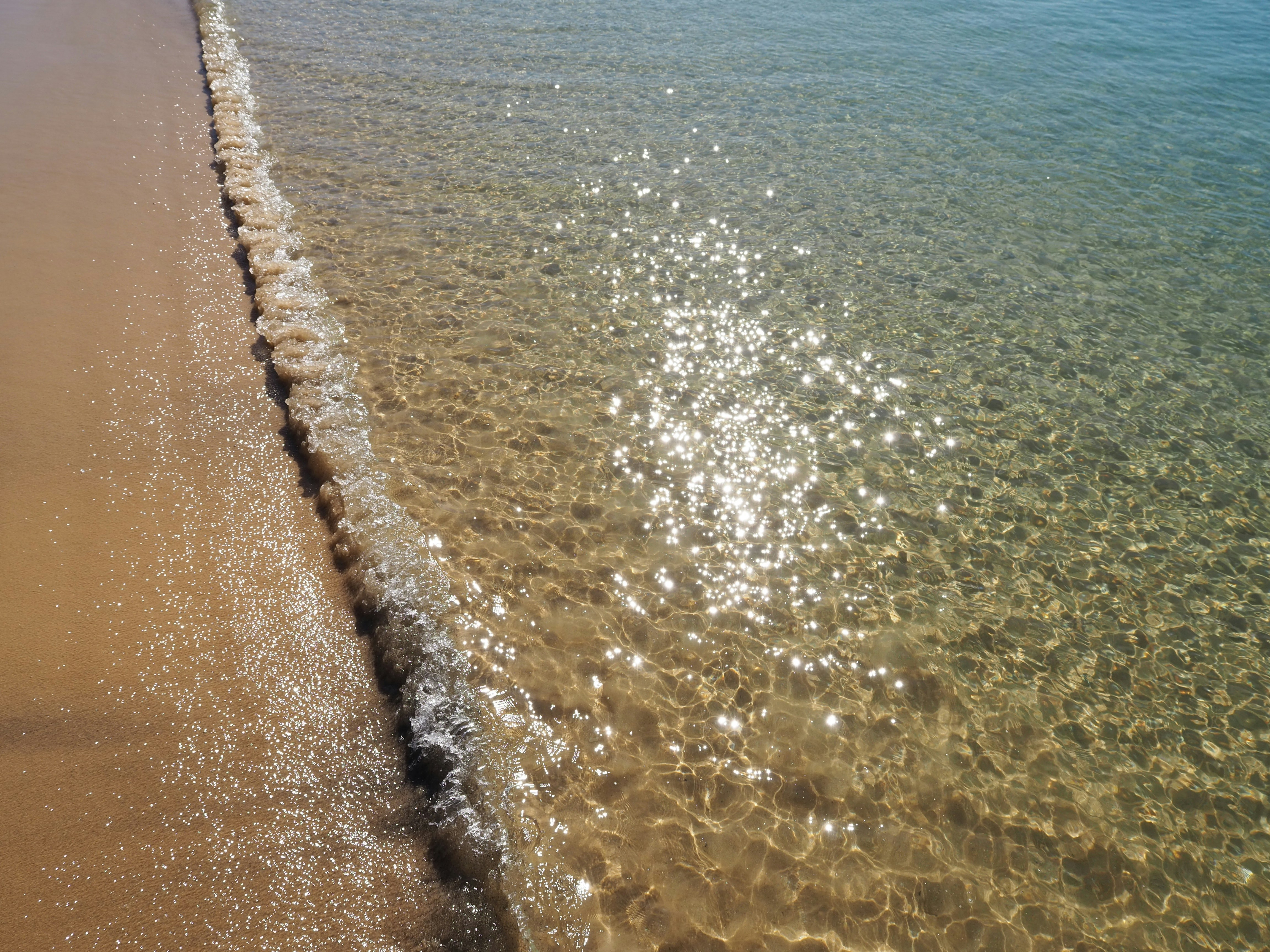 Gentle waves lap against a sunlit sandy beach, creating a shimmering dance of light on the water's surface.