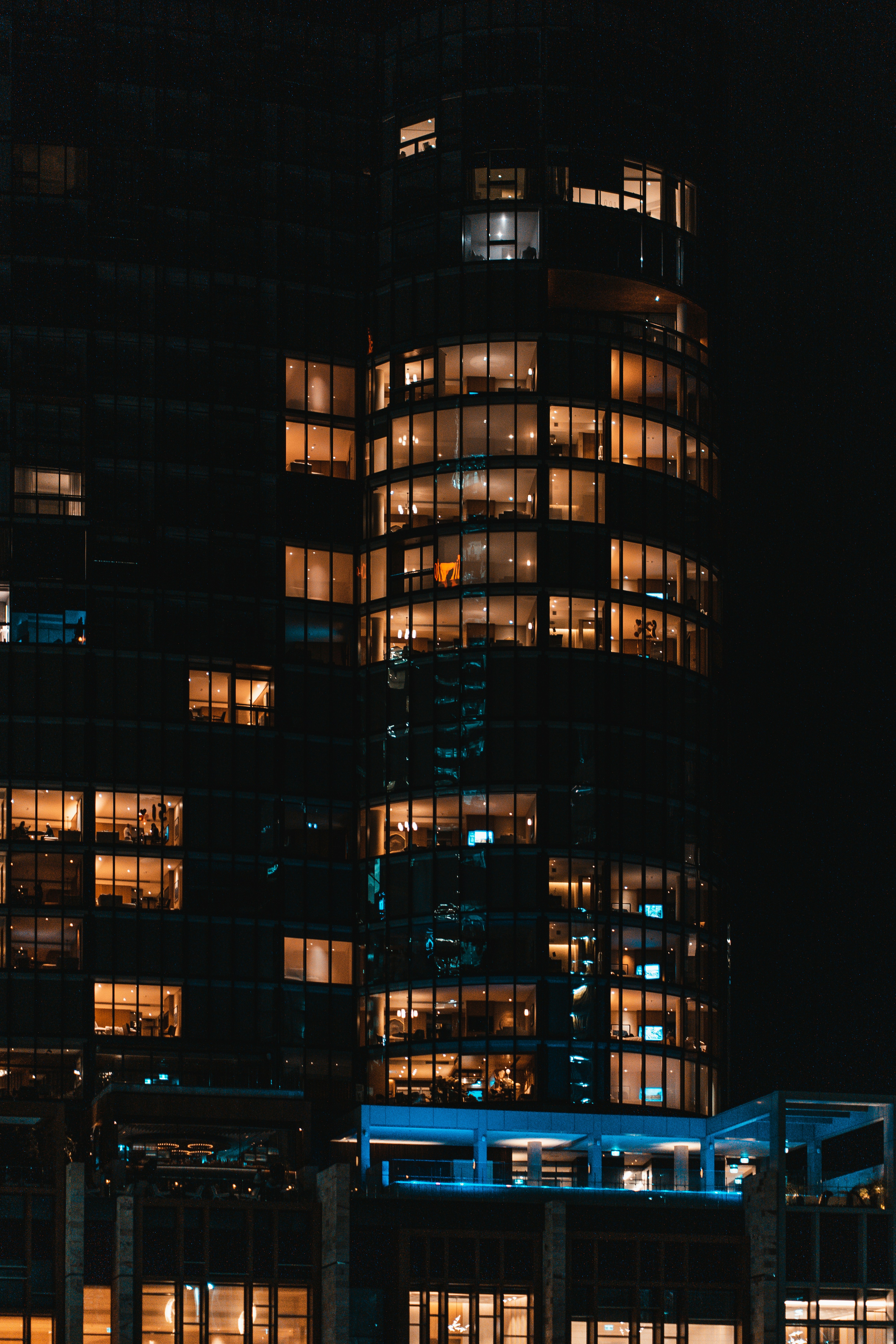 Illuminated windows of a modern skyscraper at night, showcasing the vibrant life within. The contrast of warm and cool tones creates a dynamic urban atmosphere.