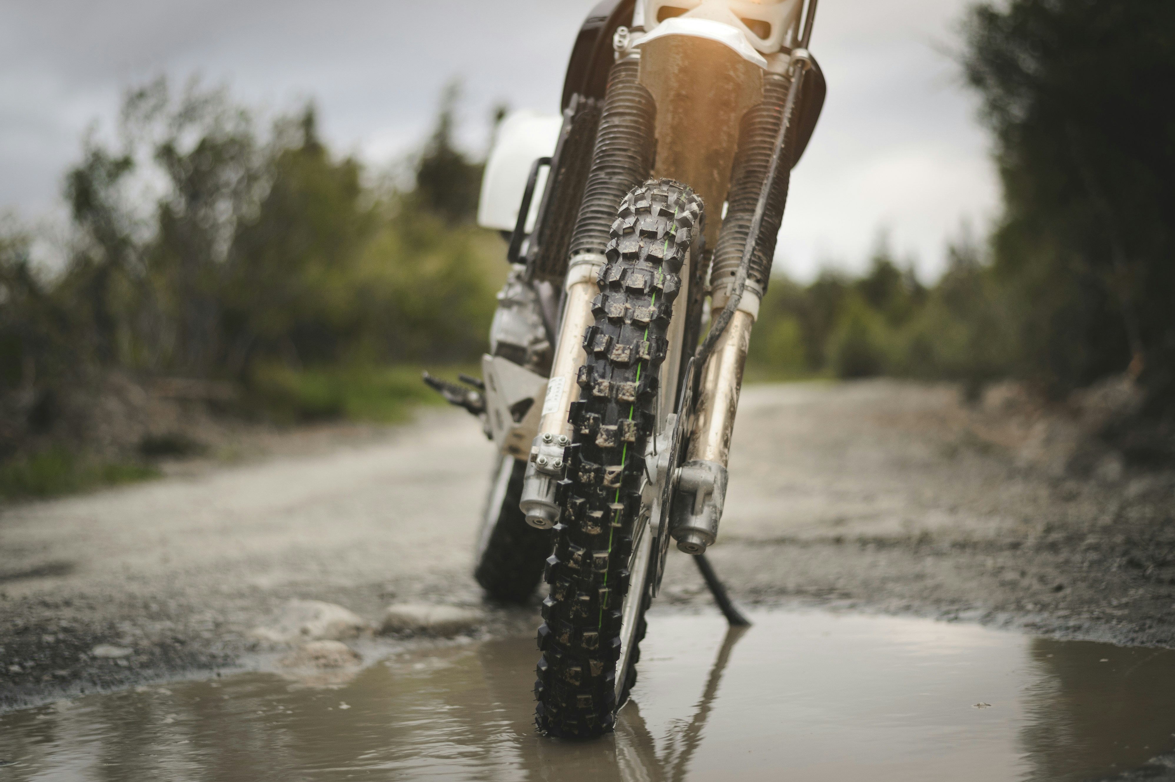 Close-up of a dirt bike tire partially submerged in a puddle on a rugged trail, showcasing the vehicle's readiness for off-road challenges.
