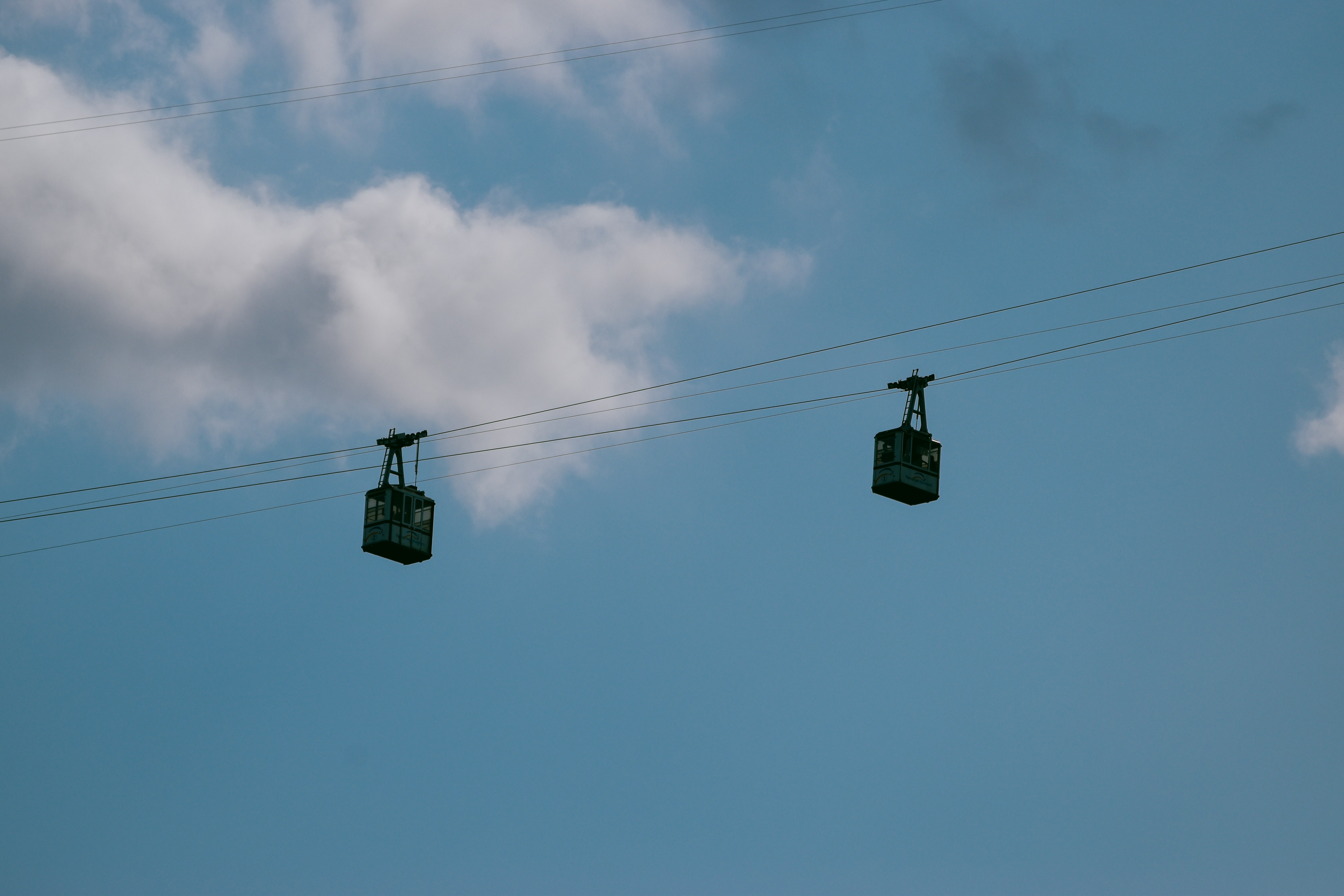 Two cable cars glide through a clear blue sky with scattered clouds.