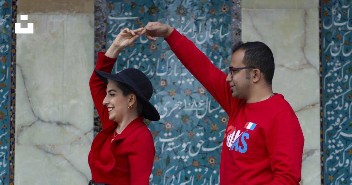 Man In Red Long Sleeve Shirt And Black Pants Standing Beside Woman In