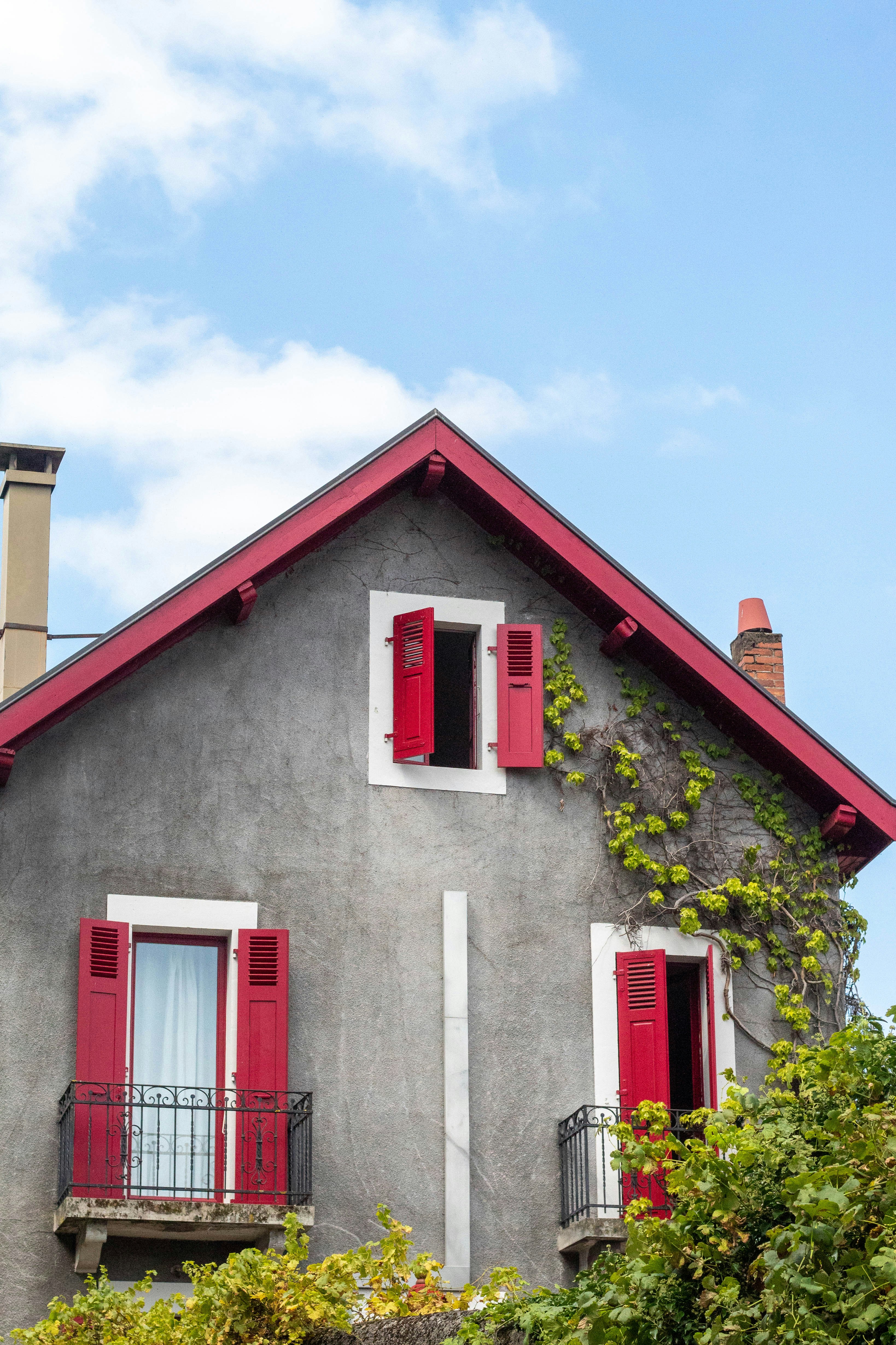 A quaint house featuring vibrant red shutters and a touch of greenery, set against a clear blue sky.