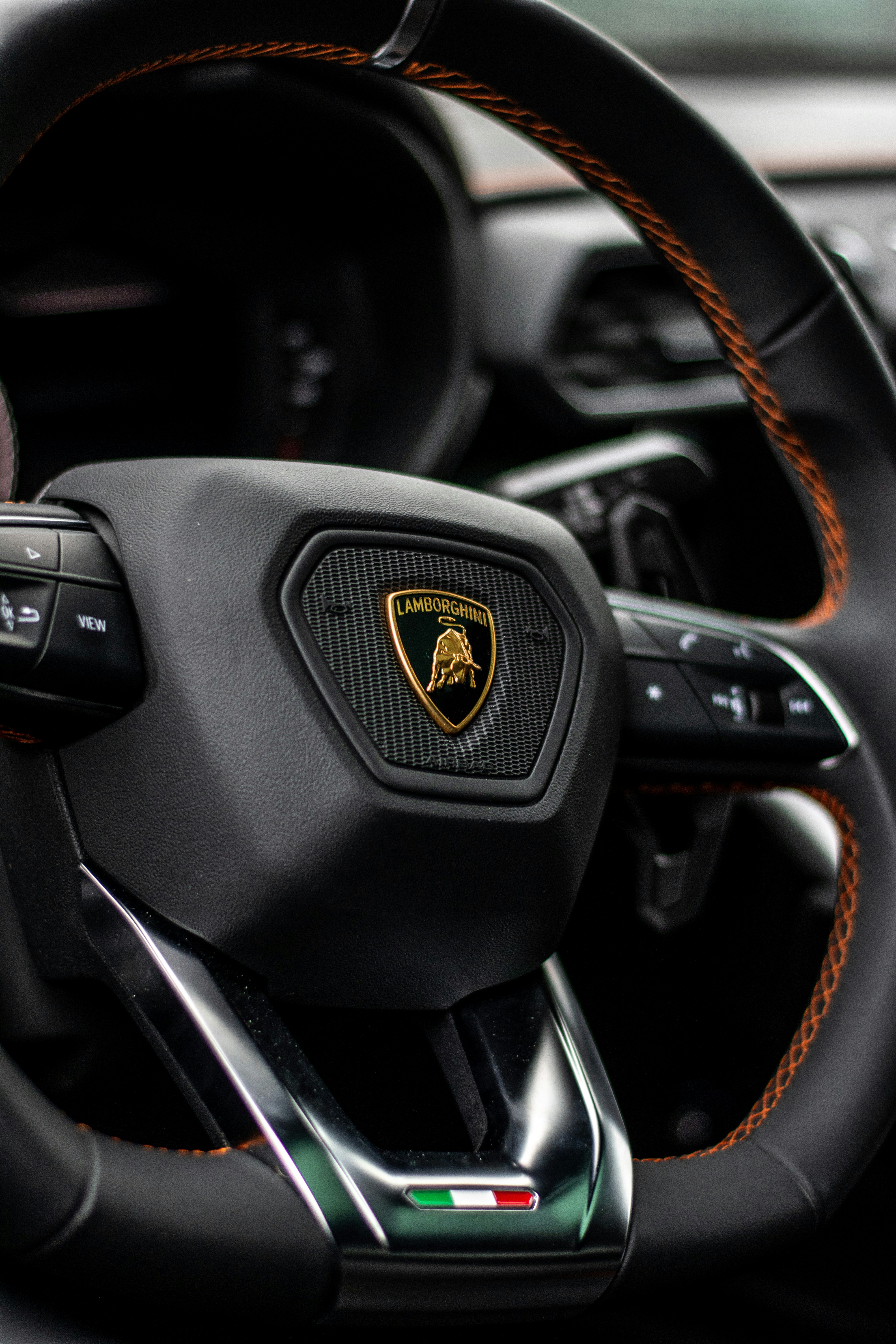 Close-up of a Lamborghini steering wheel featuring the iconic logo and intricate design details. The craftsmanship highlights the luxury sports car experience.