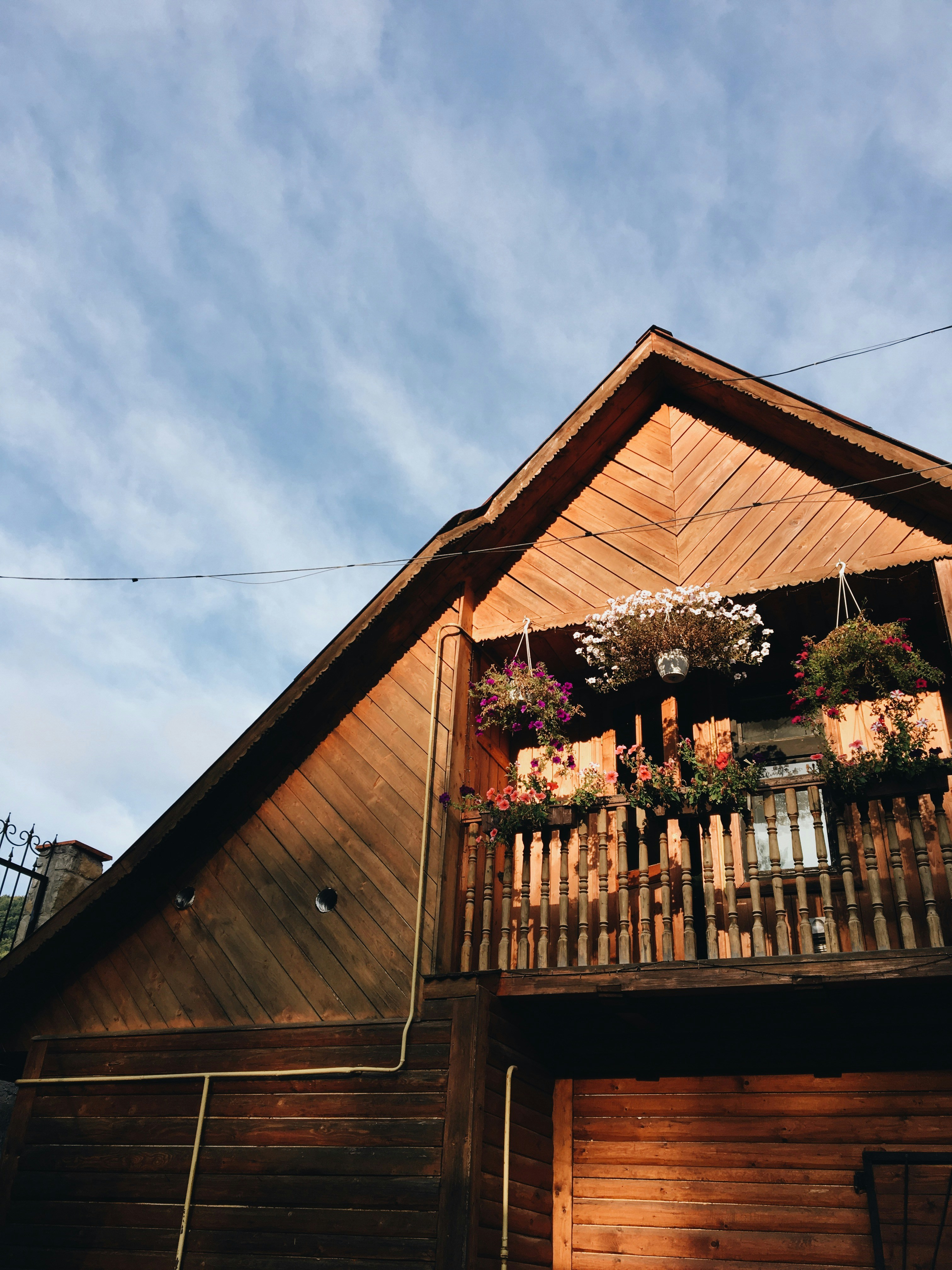 A rustic wooden house featuring a balcony adorned with vibrant flowers, set against a clear blue sky.