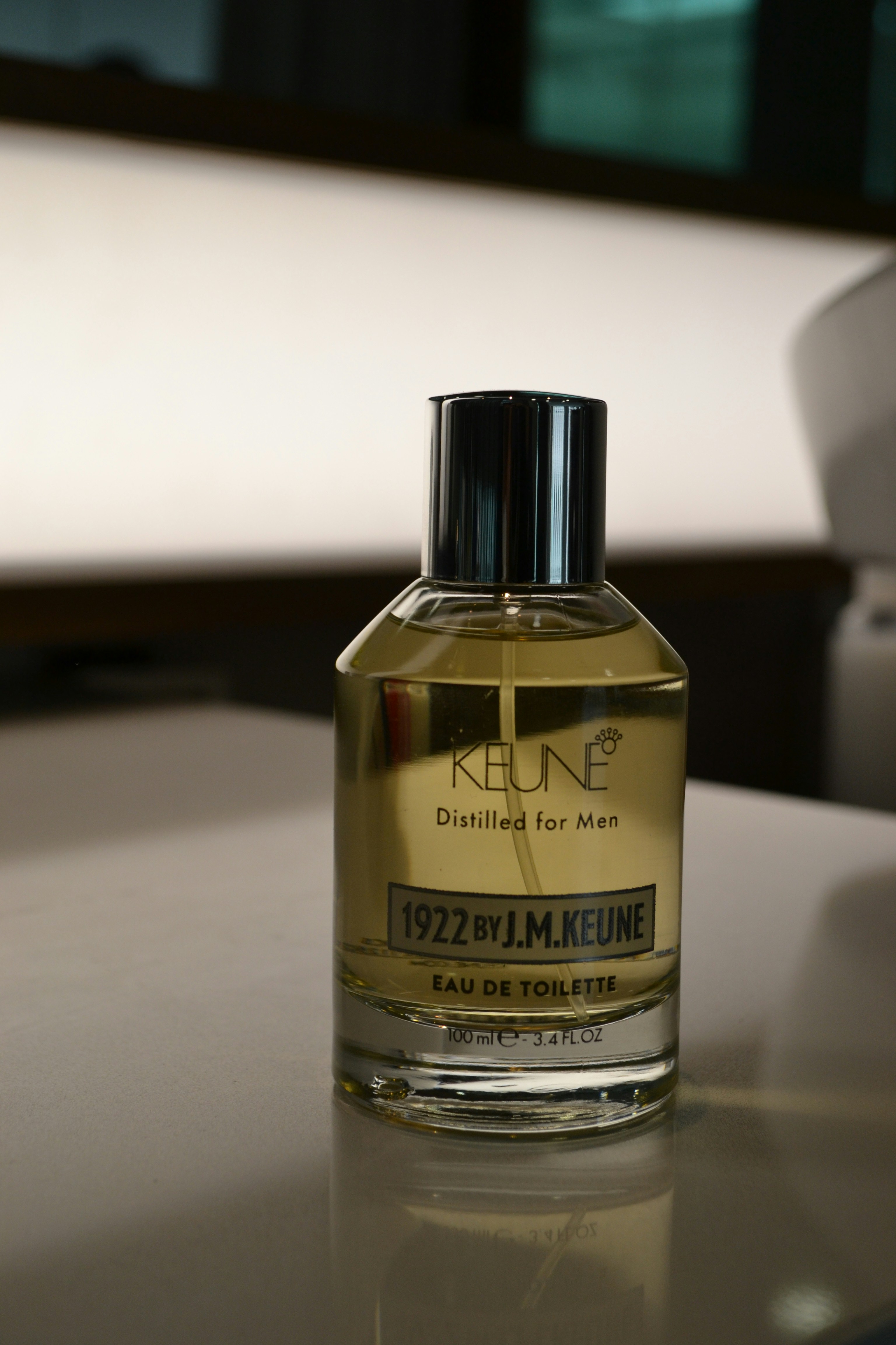 Elegant perfume bottle of KEUNE's 1922 by J.M. KEUNE, showcasing its refined design and golden liquid against a softly lit background.