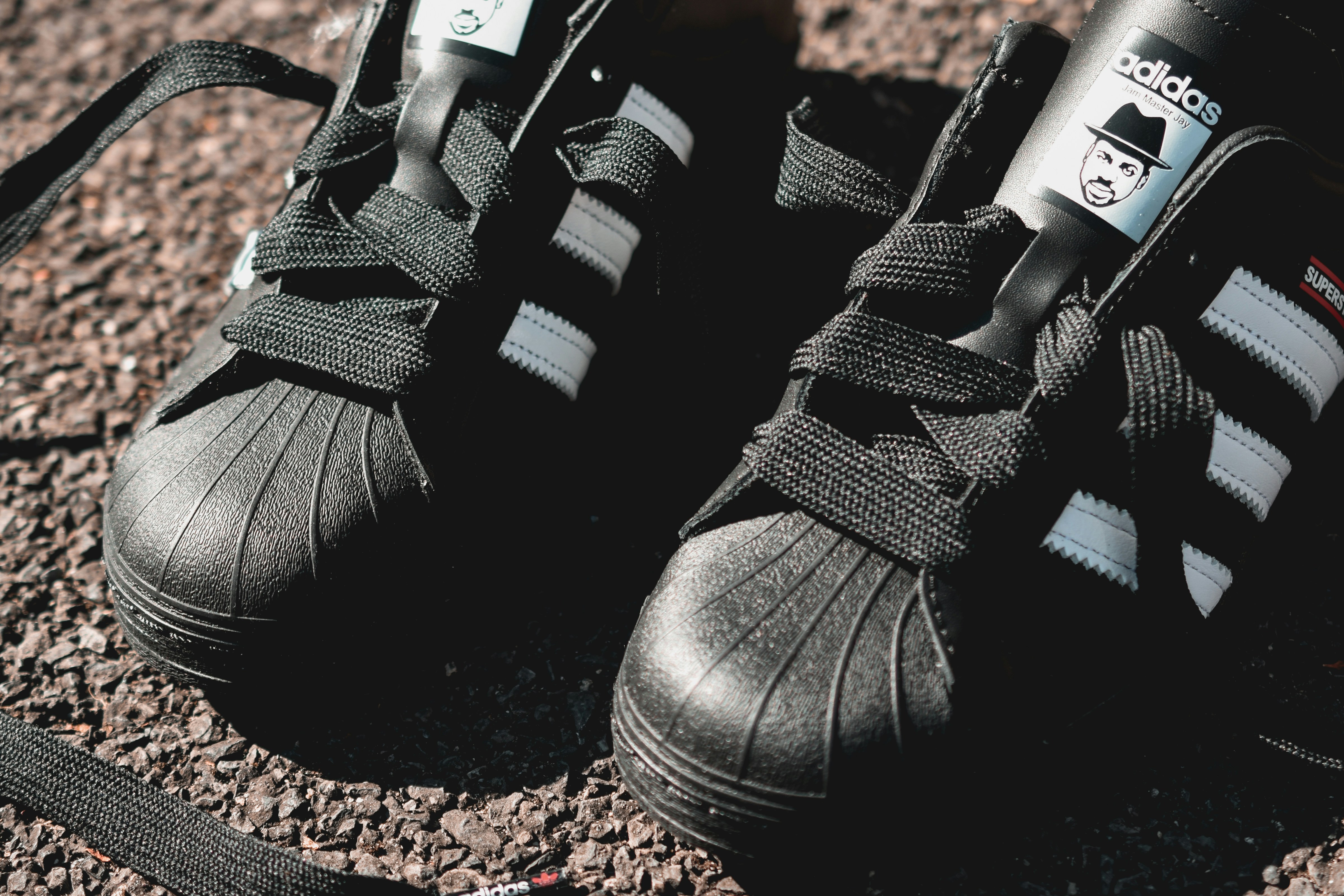 Black Adidas sneakers with distinctive shell toes and laces resting on a textured surface, showcasing a unique design element.