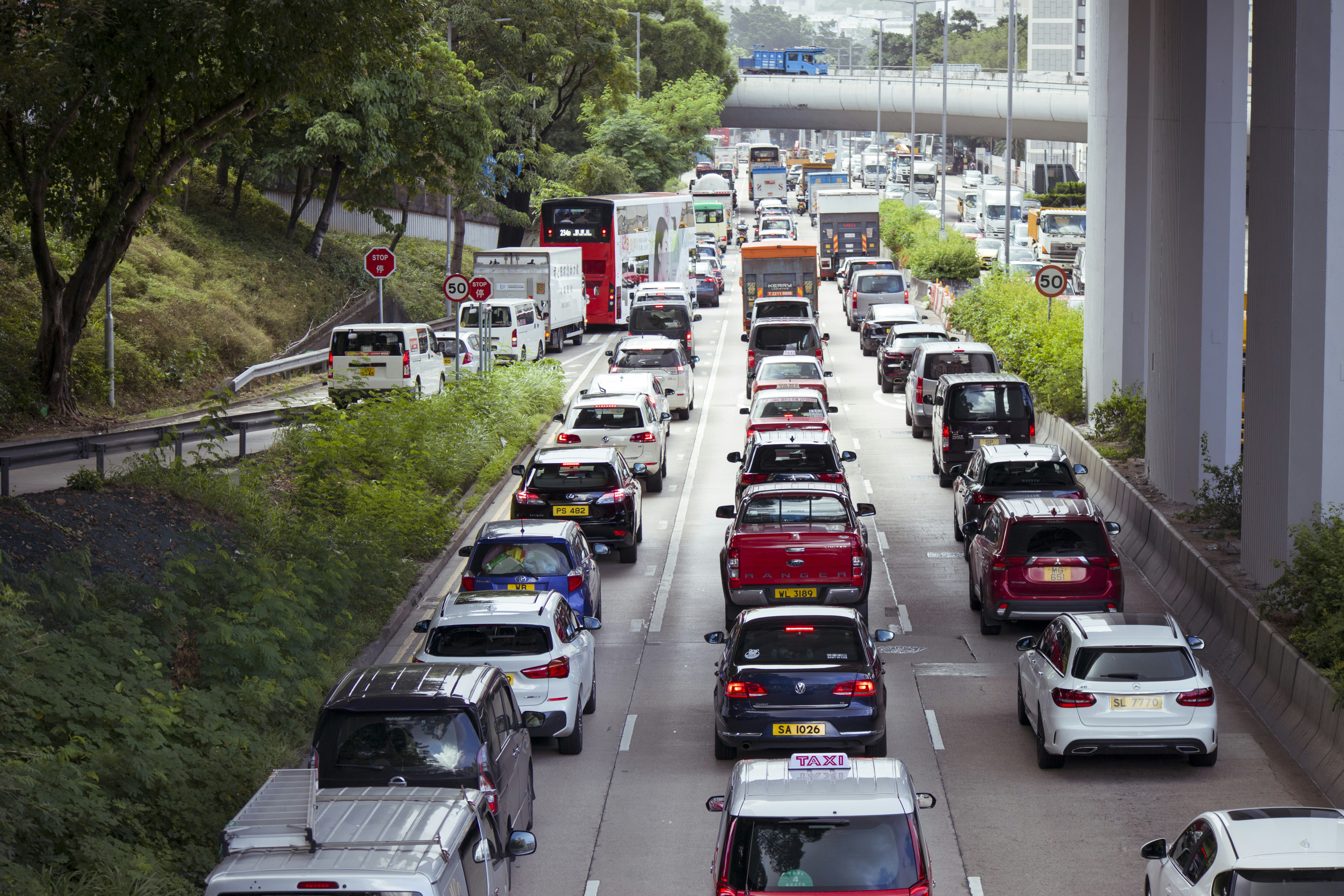 Dense traffic on a multi-lane highway flanked by greenery and city infrastructure.