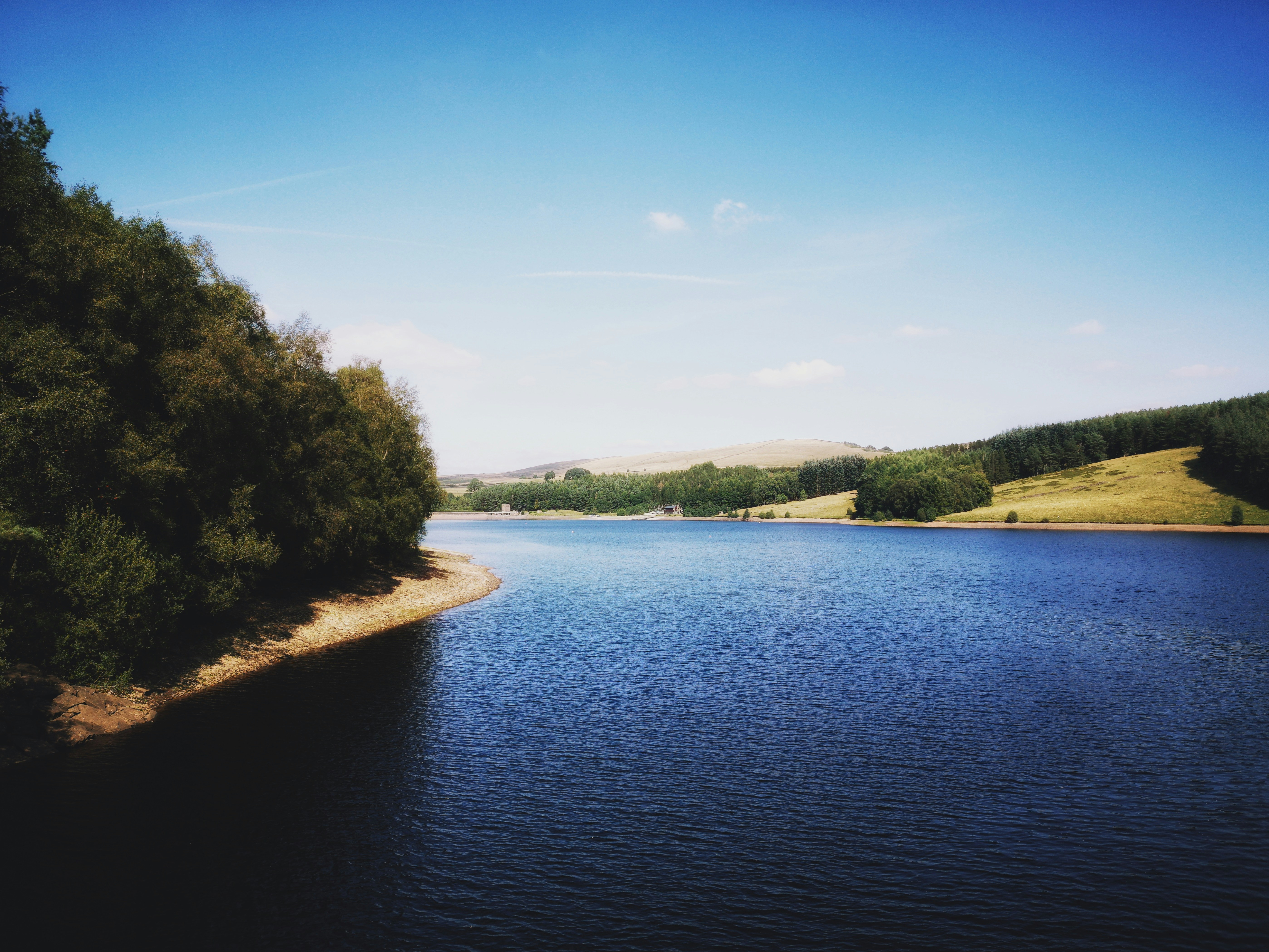 Tranquil lake surrounded by lush greenery and rolling hills under a clear blue sky.