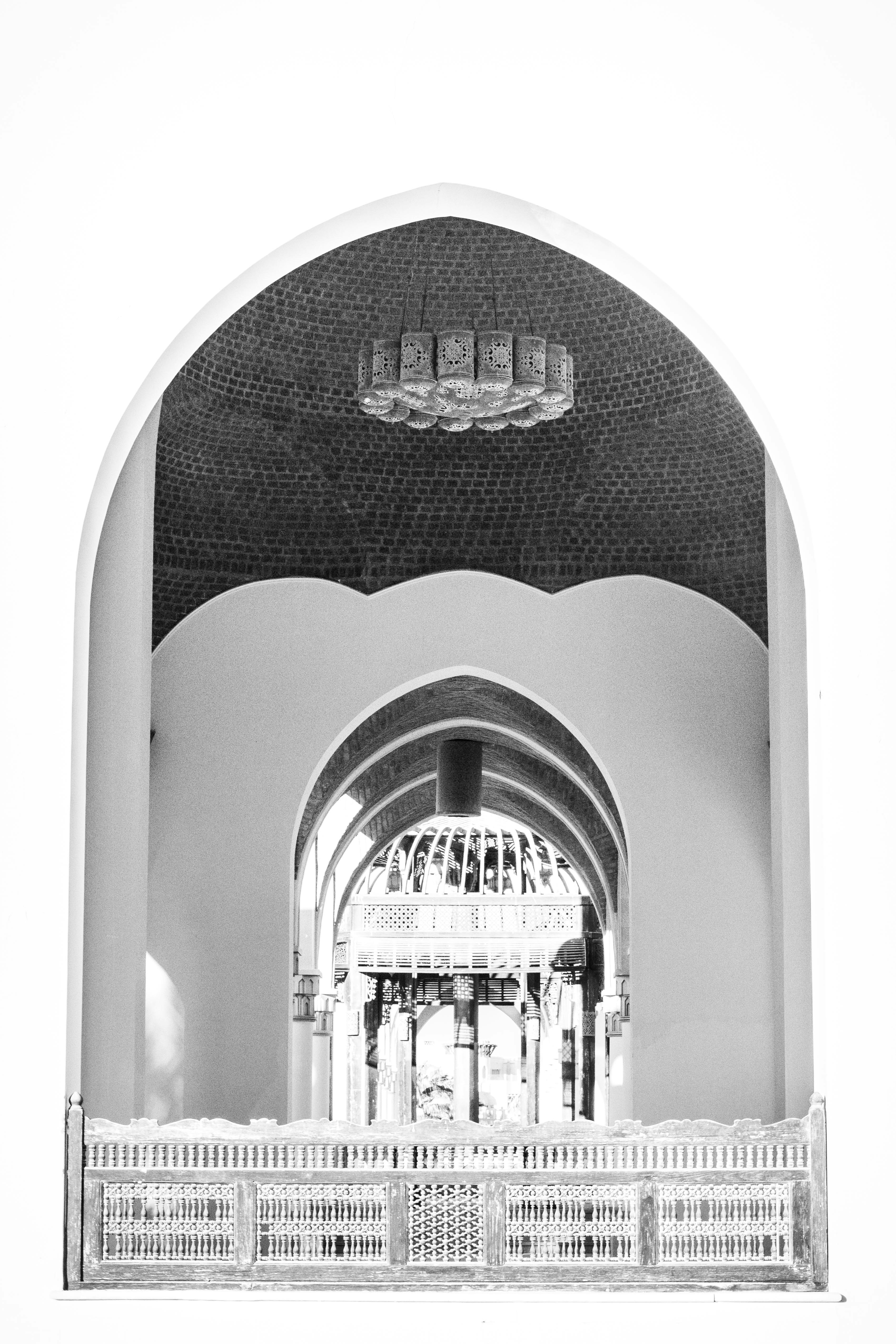 Intricate arches frame a luminous chandelier in a minimalist interior, showcasing a blend of traditional and modern design elements.