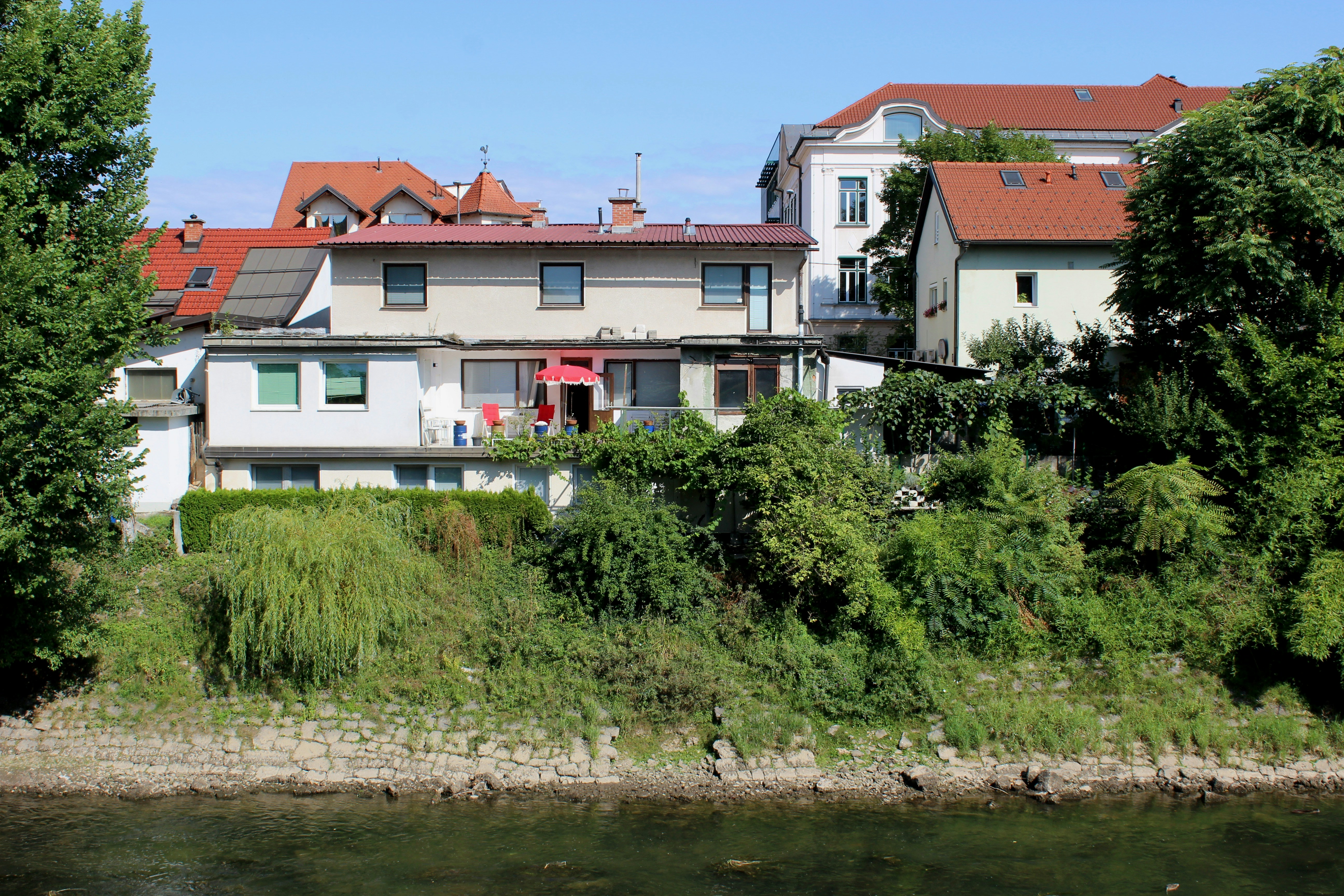 White and brown concrete house beside green trees and body of water ...