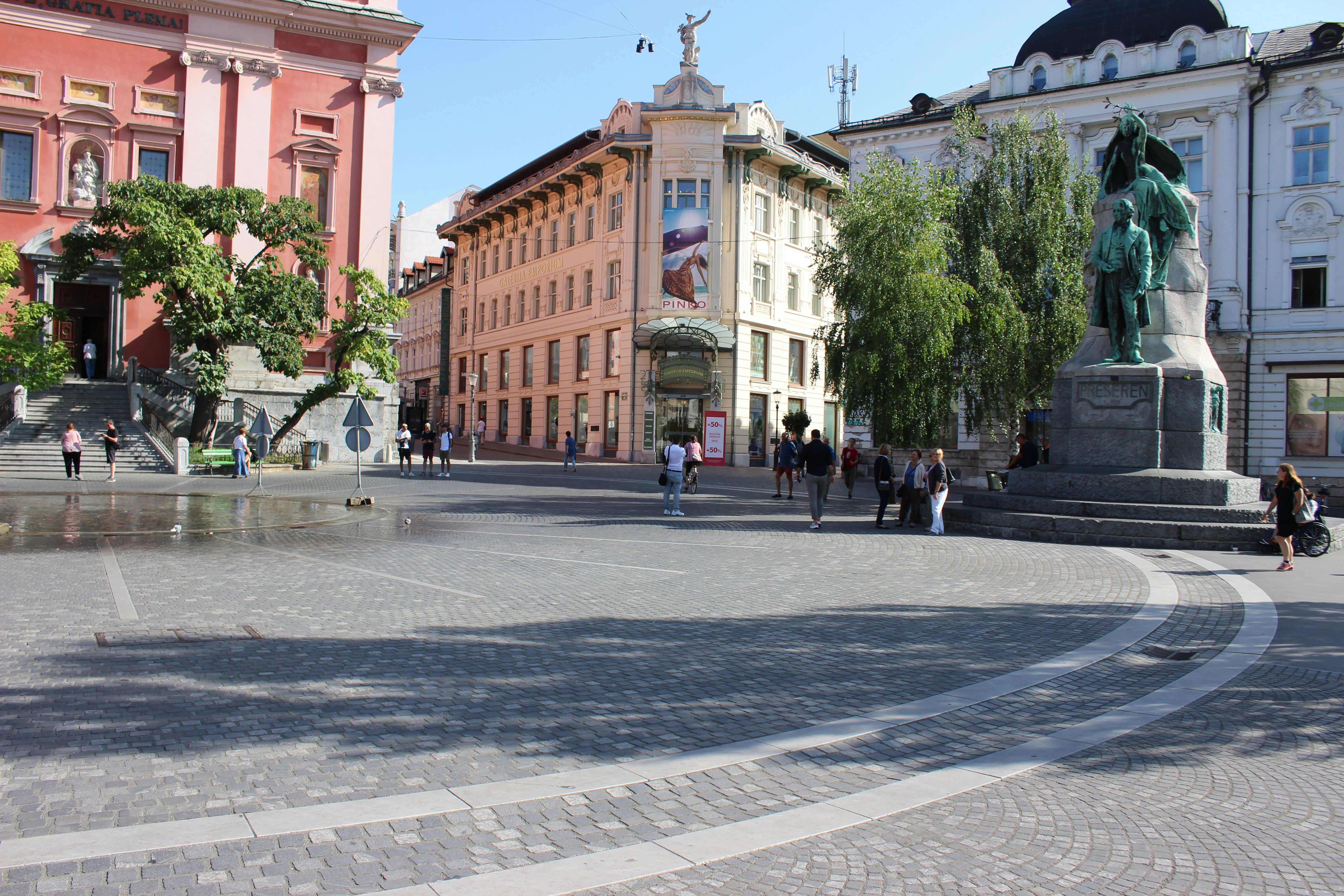 Sunny square in Ljubljana with a prominent statue and surrounding historic buildings.