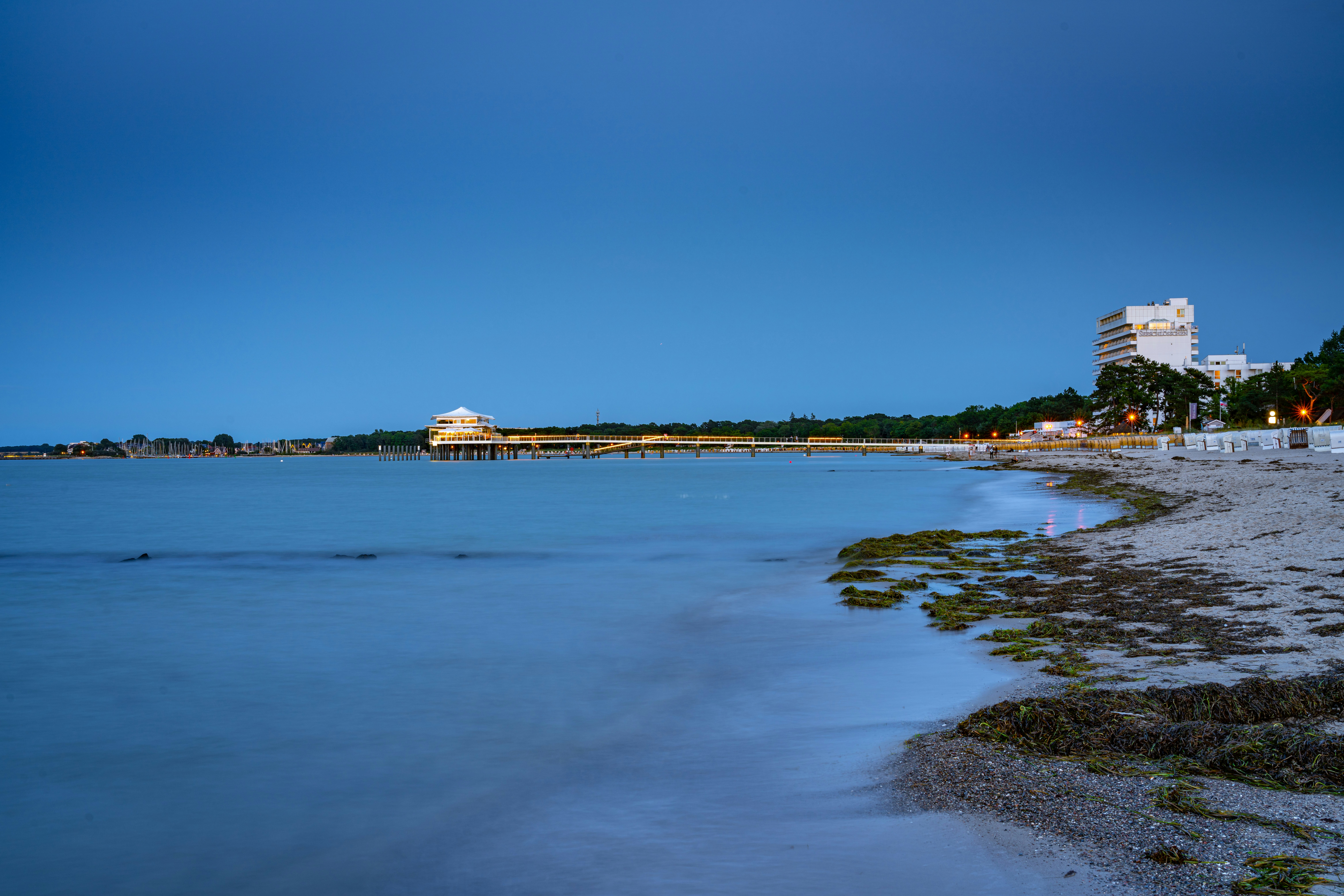 Blue-Hour Horizon: Quiet Seaside Pier Framed by Calm Waters and Mossy Rocks