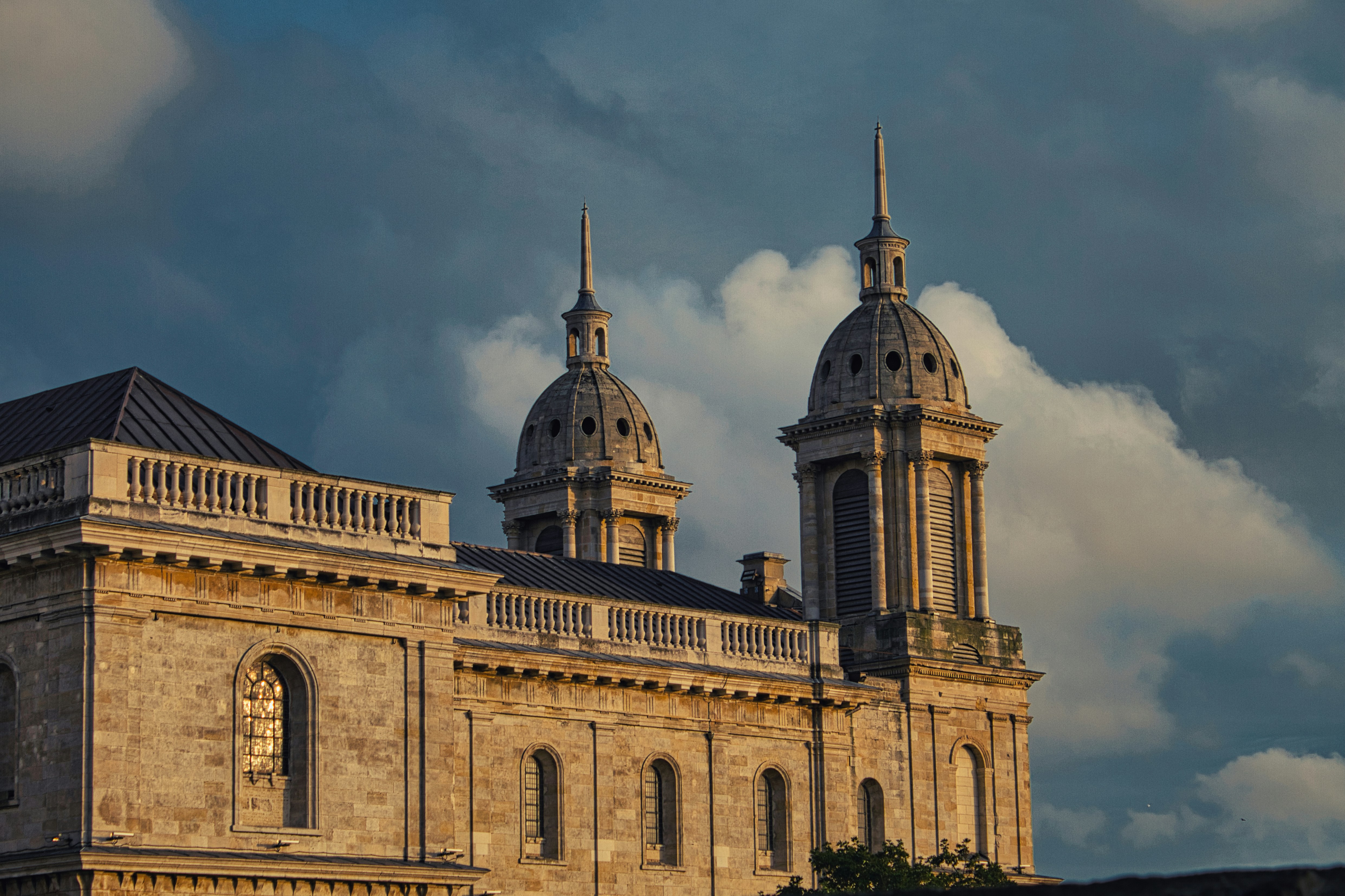 Historic building featuring twin spires under a dramatic cloud backdrop. The architecture showcases intricate details and textures.