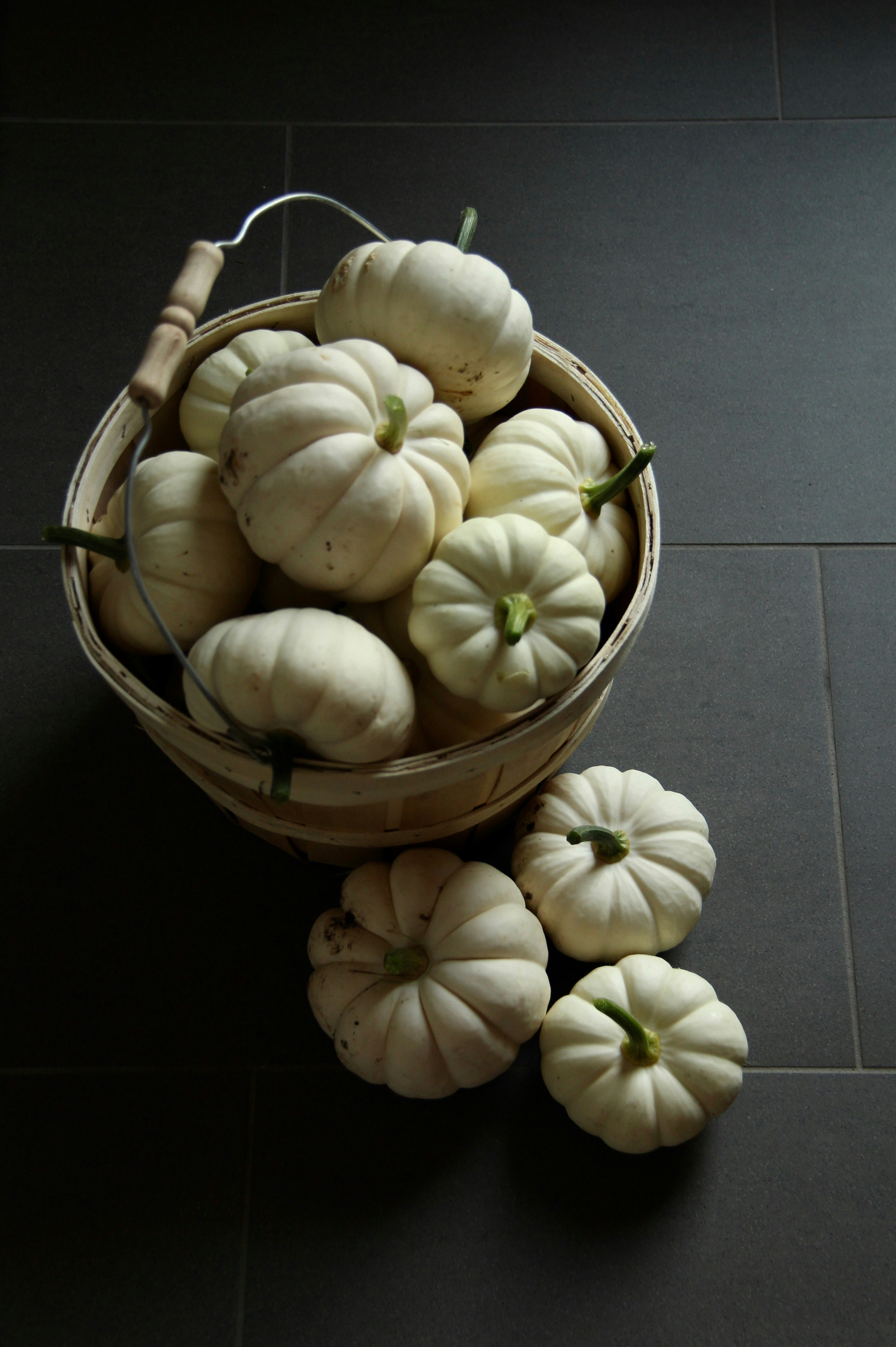 White pumpkins in a wooden basket spill onto a dark tiled floor