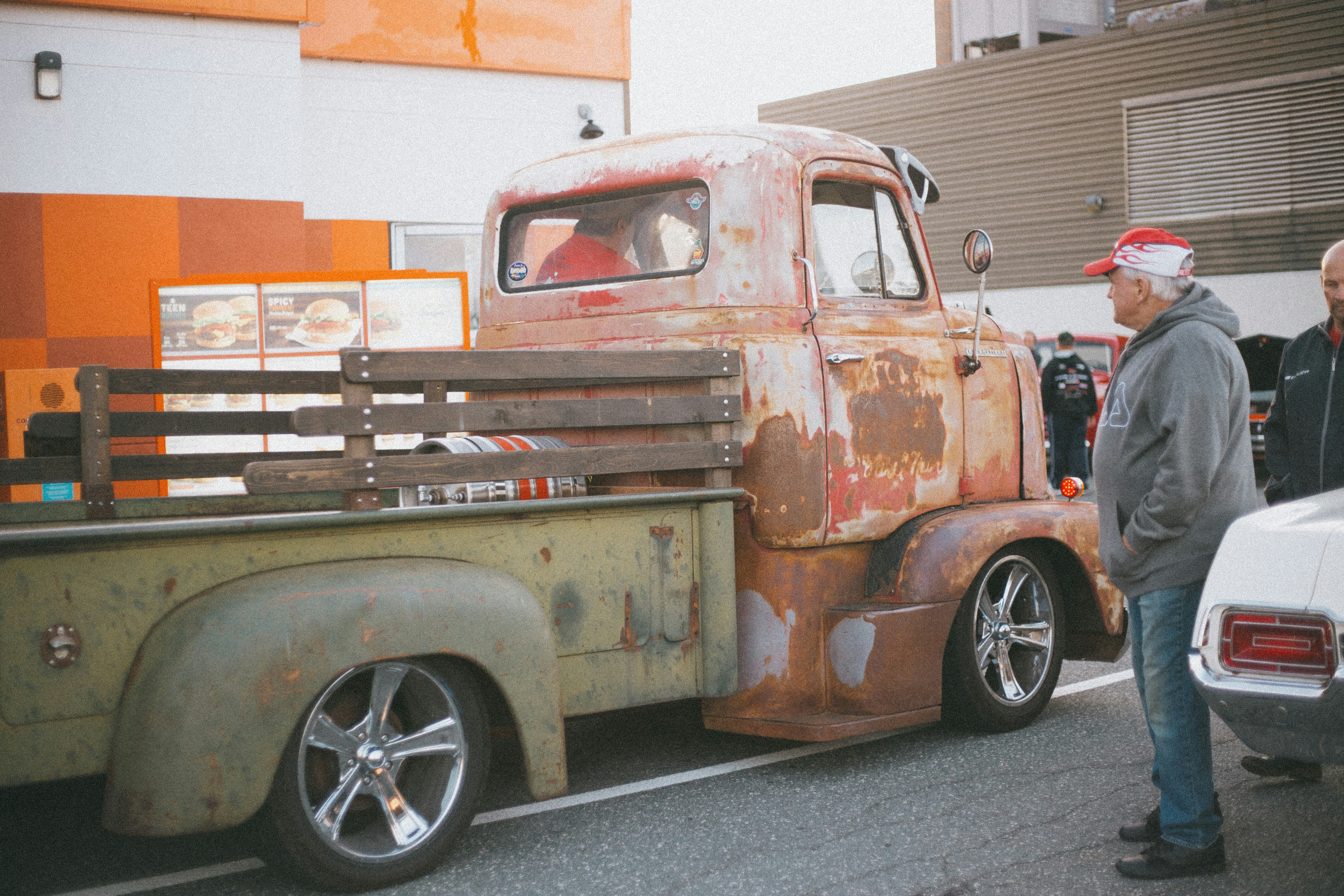 Vintage truck with a weathered exterior parked beside a fast-food restaurant, showcasing its unique character and retro design.