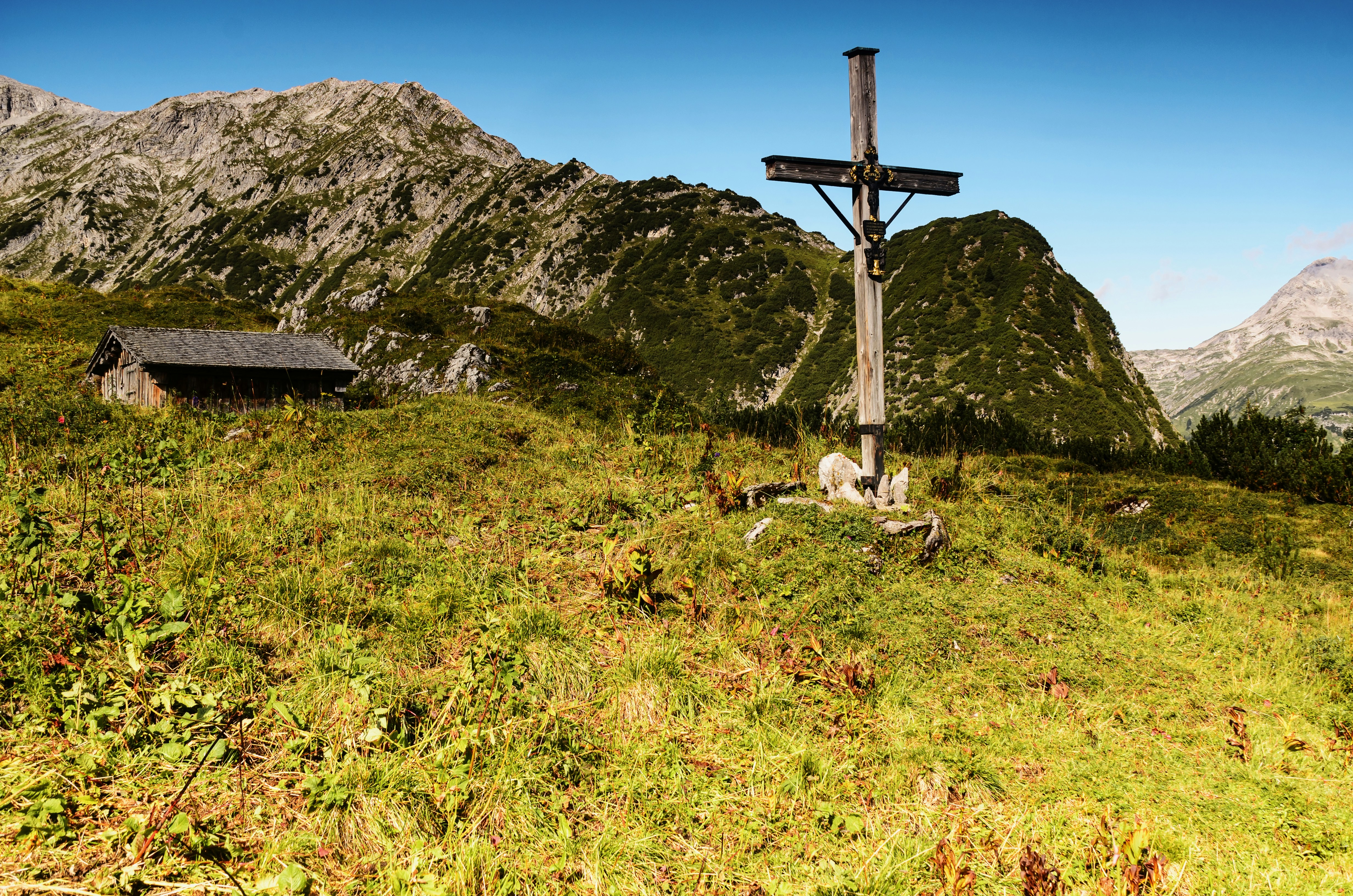 Lone Alpine Cross Standing Guard Over a Lush Meadow Beneath Towering Peaks