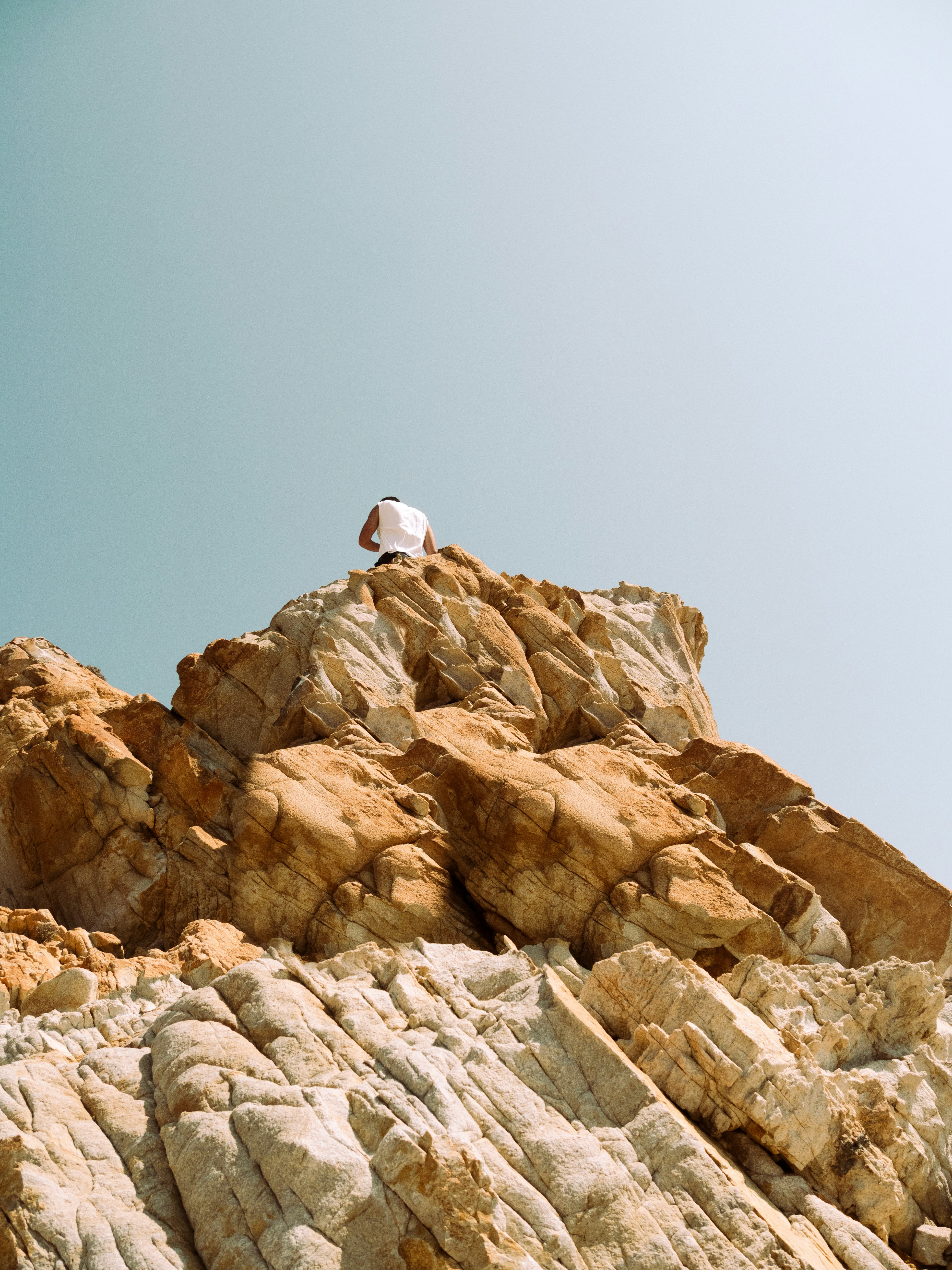 A figure stands atop a rugged rock formation, gazing into the distance under a clear sky. The textured layers of stone contrast with the serene backdrop.
