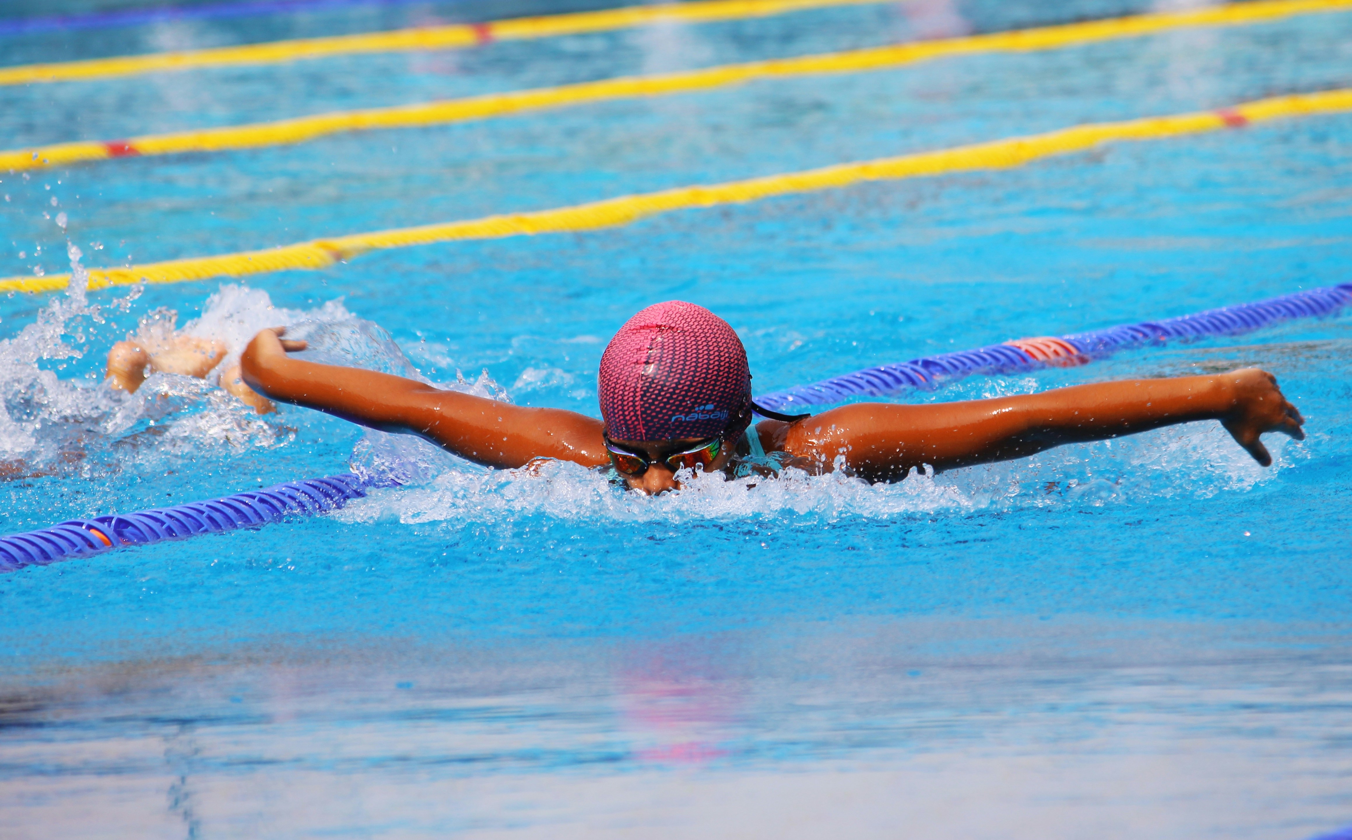 Young swimmer executing a butterfly stroke in a vibrant pool, showcasing determination and skill during a race.