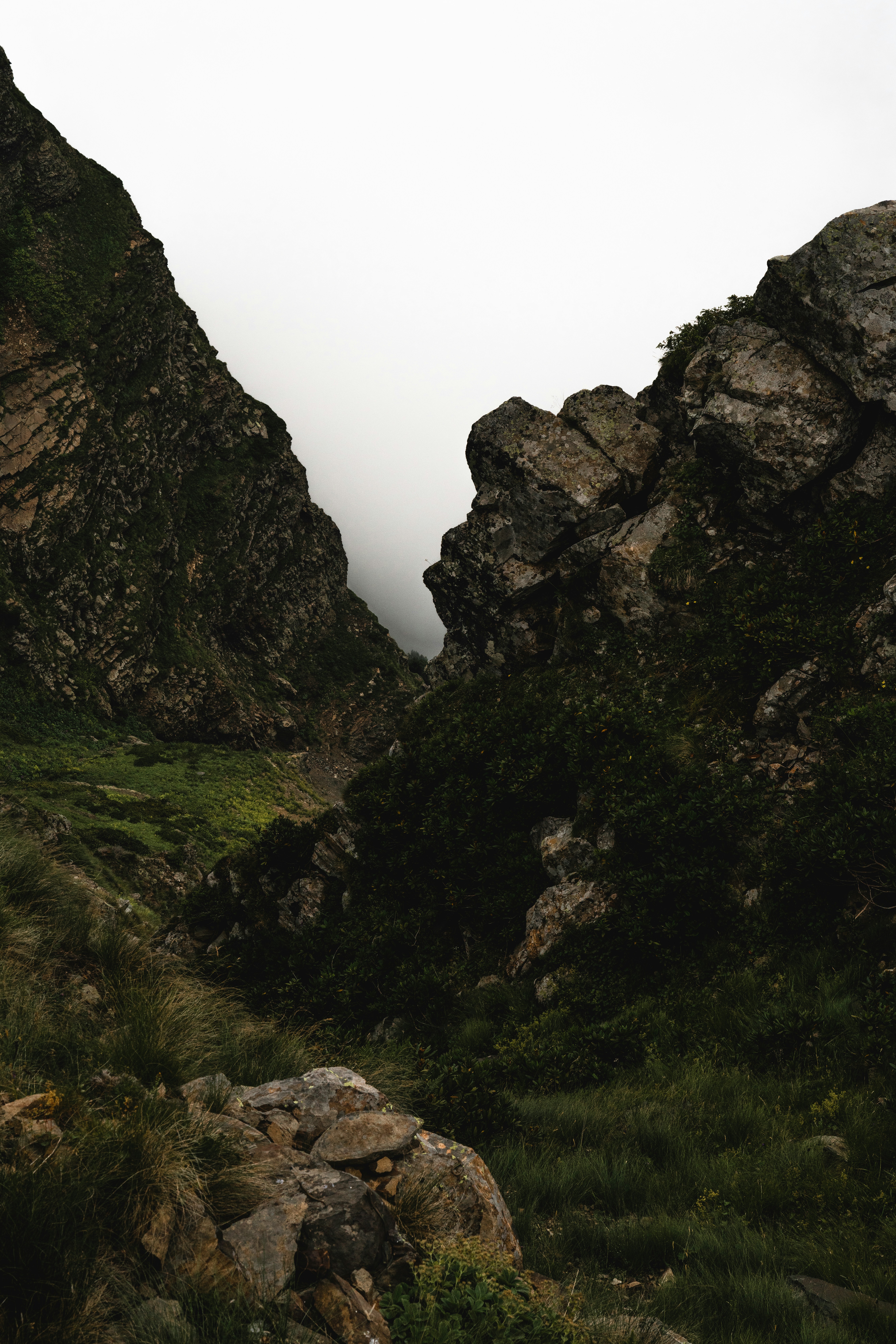 Dramatic rock formations frame a narrow, misty passage in a lush green valley.