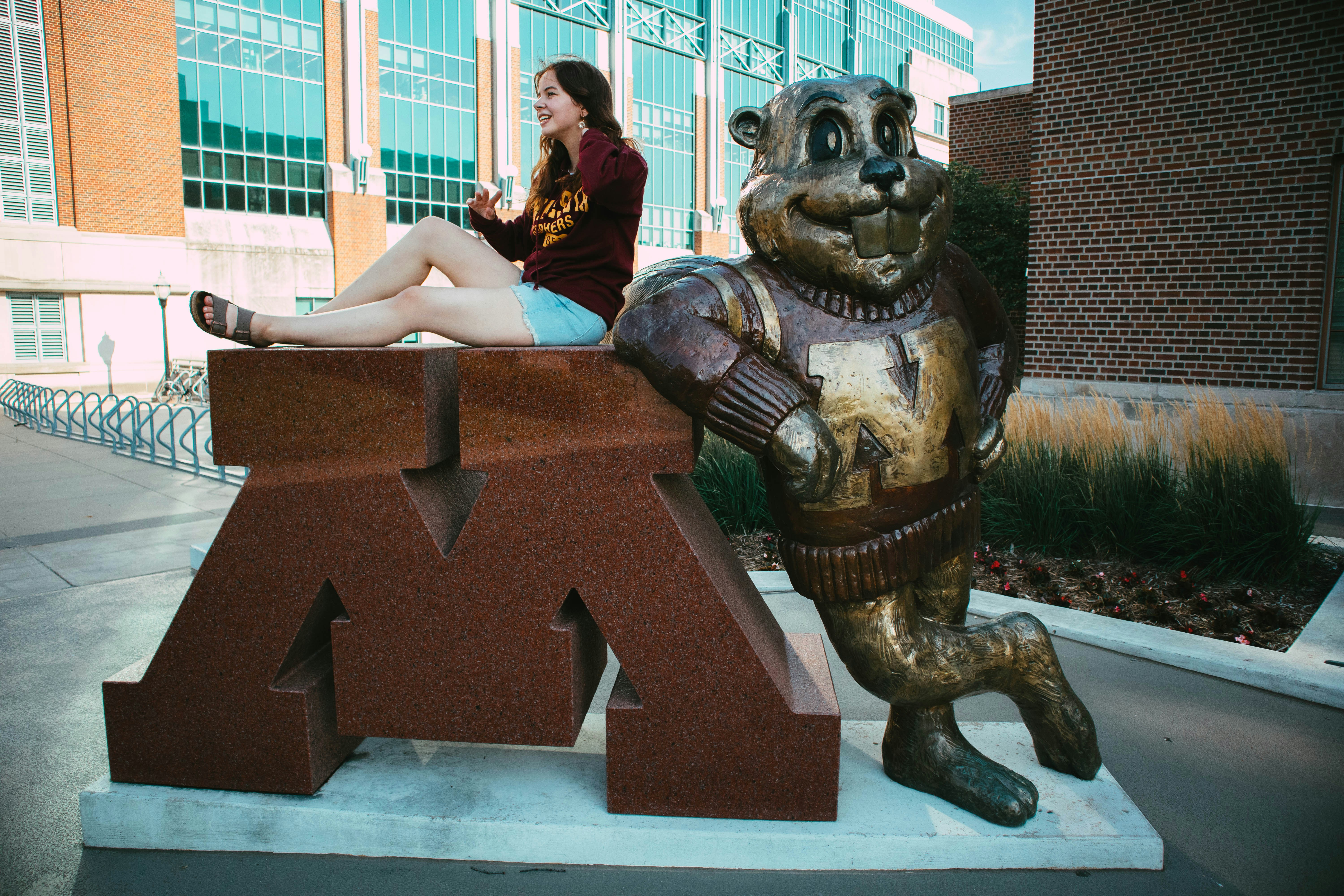 Girl Perched on a Rusted A Sculpture Beside a Bronze Bear in a University Plaza